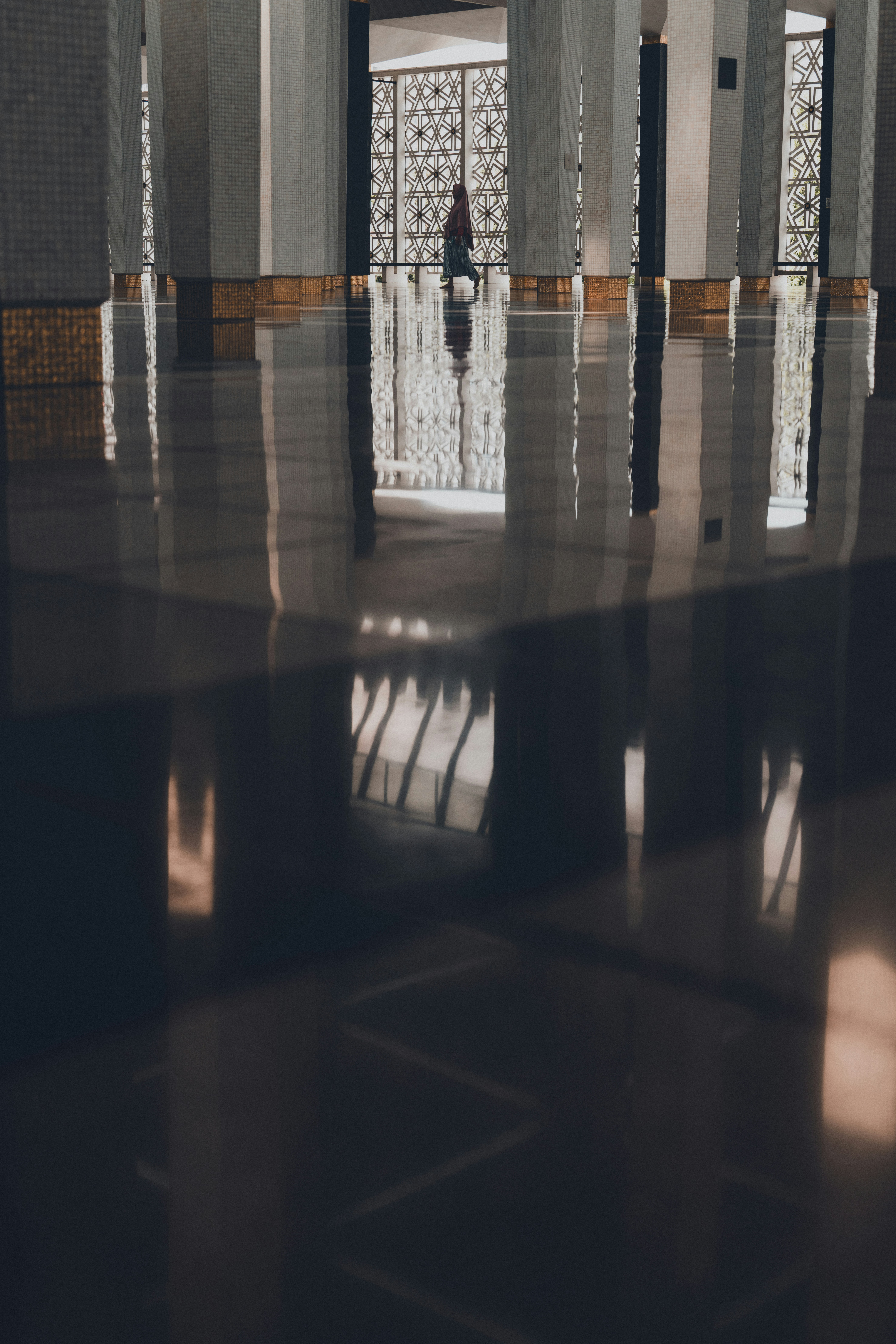  solitary figure walking through a reflective colonnade hall