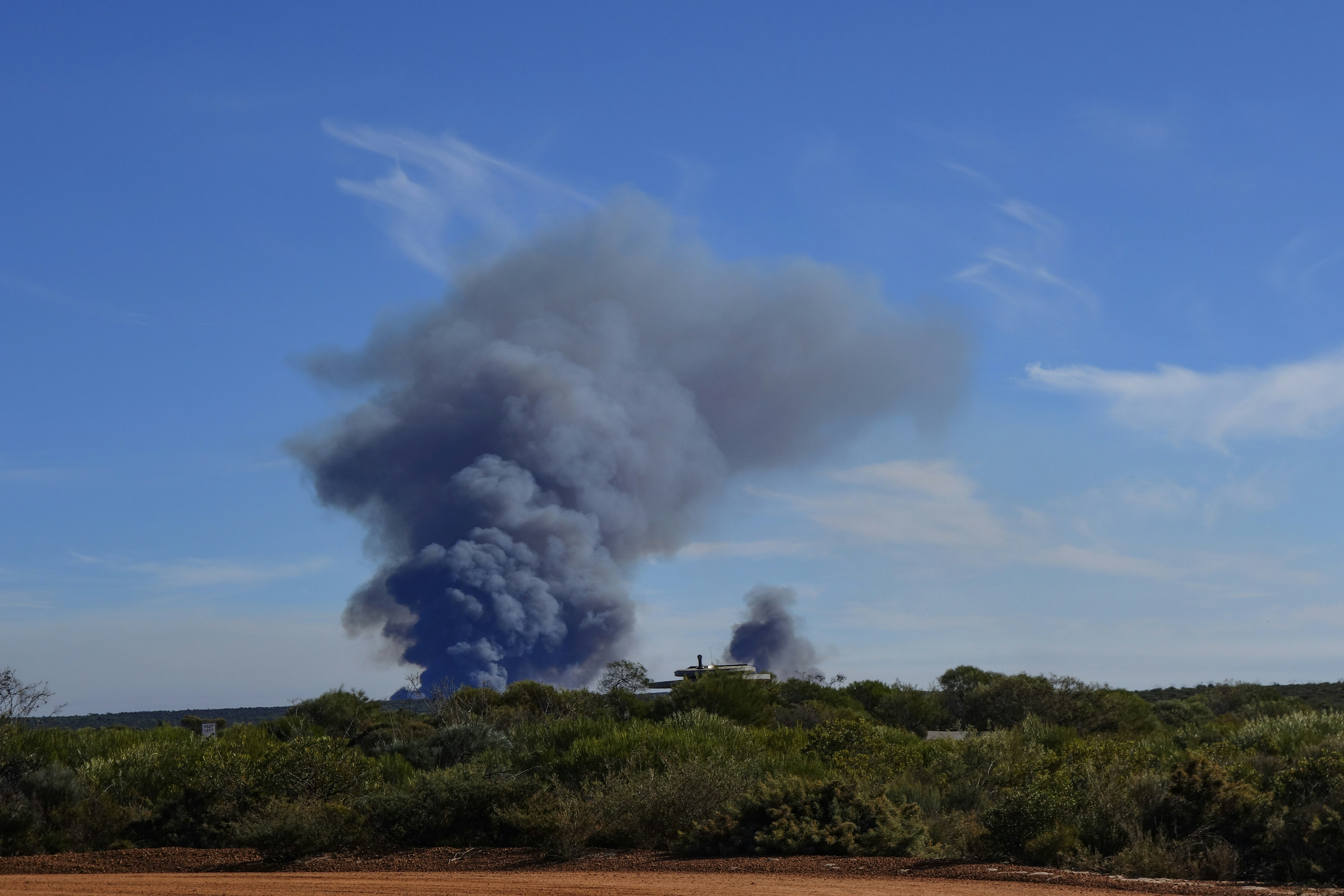 Smoke plume rises from distant scrubland on a flat horizon
