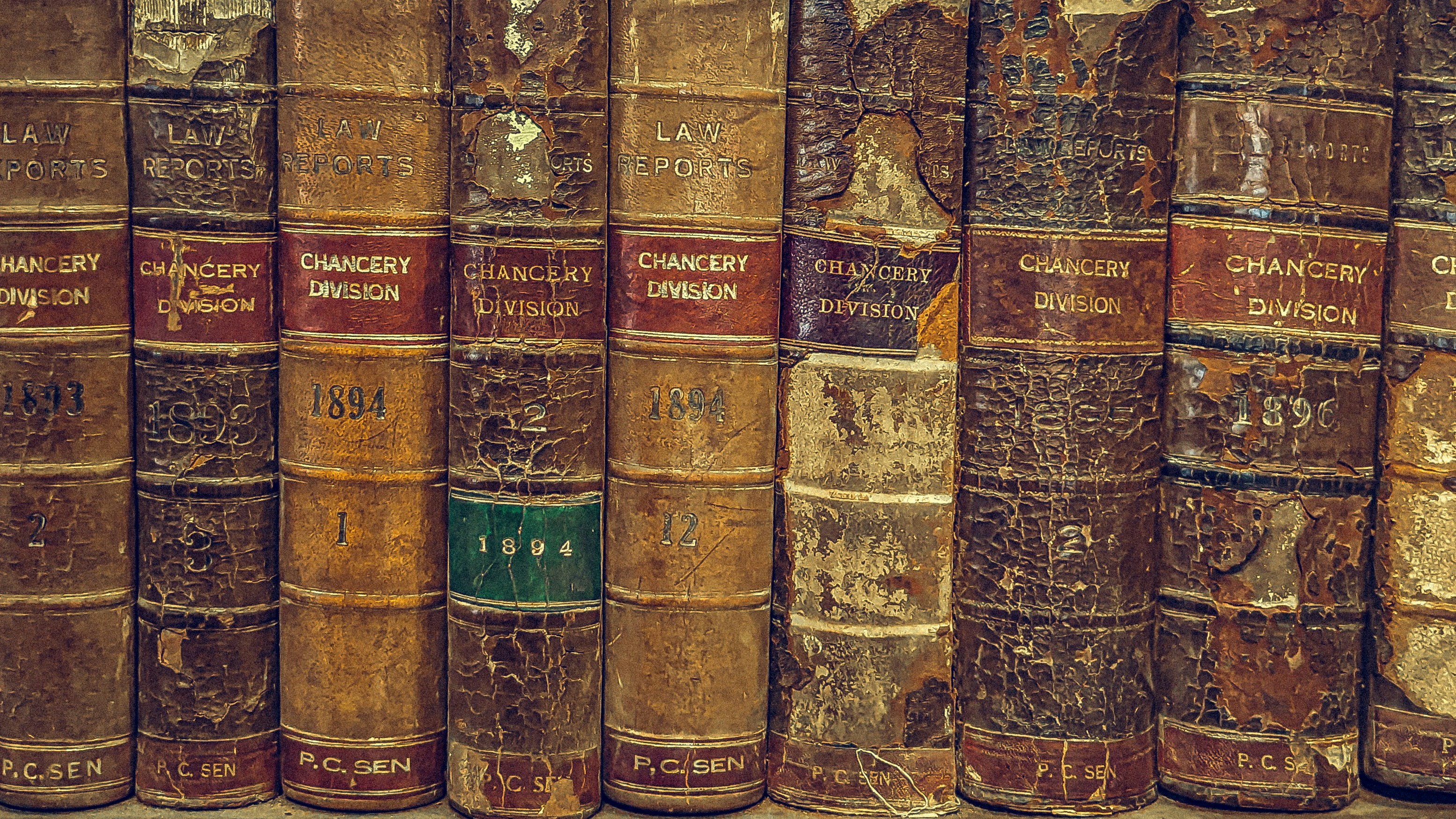 Row of aged law volumes with stained bindings and embossed spines arranged on a shelf. The scene emphasizes texture and history, suggesting archival study or antique collections.