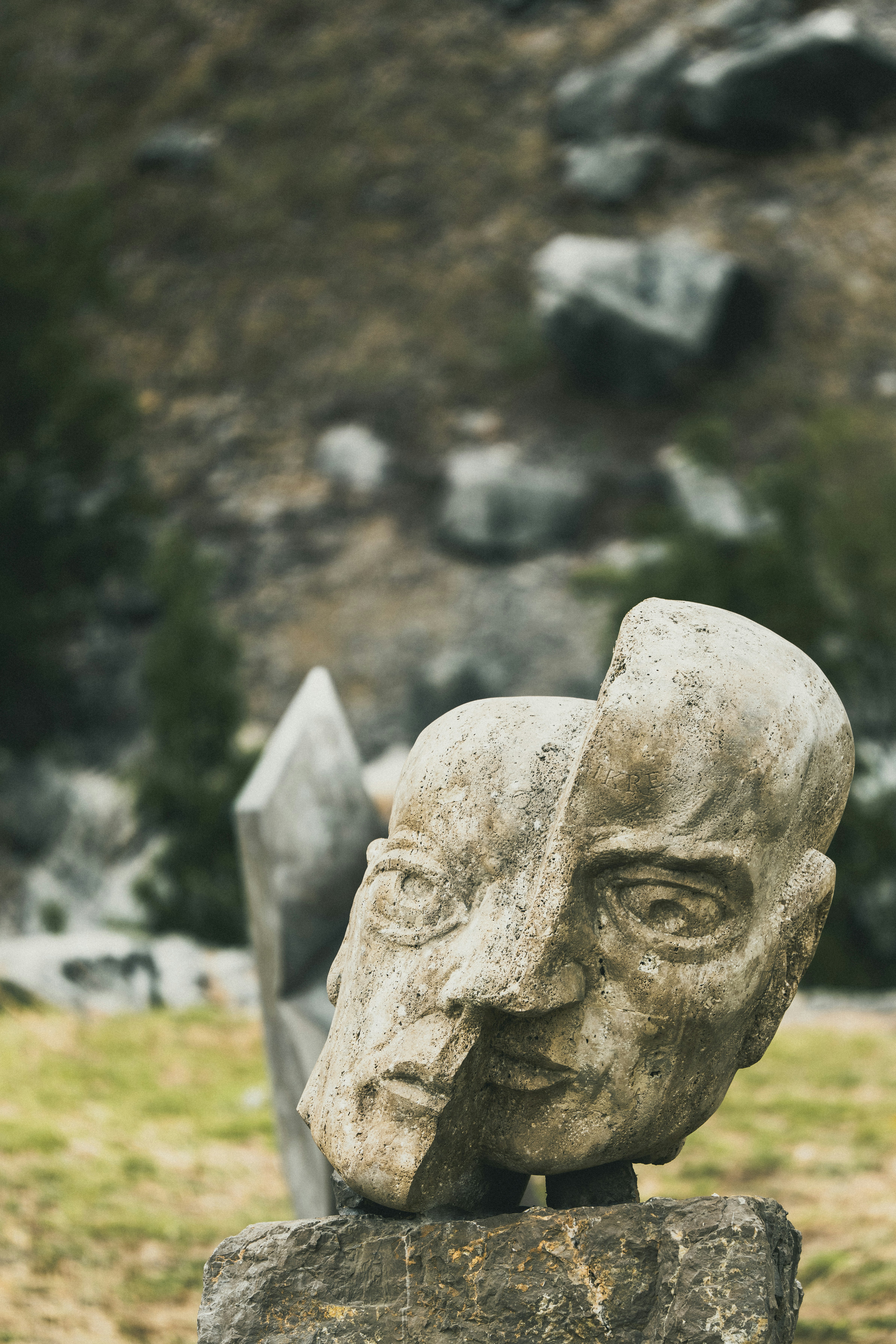 A stone sculpture of a split human head outdoors.