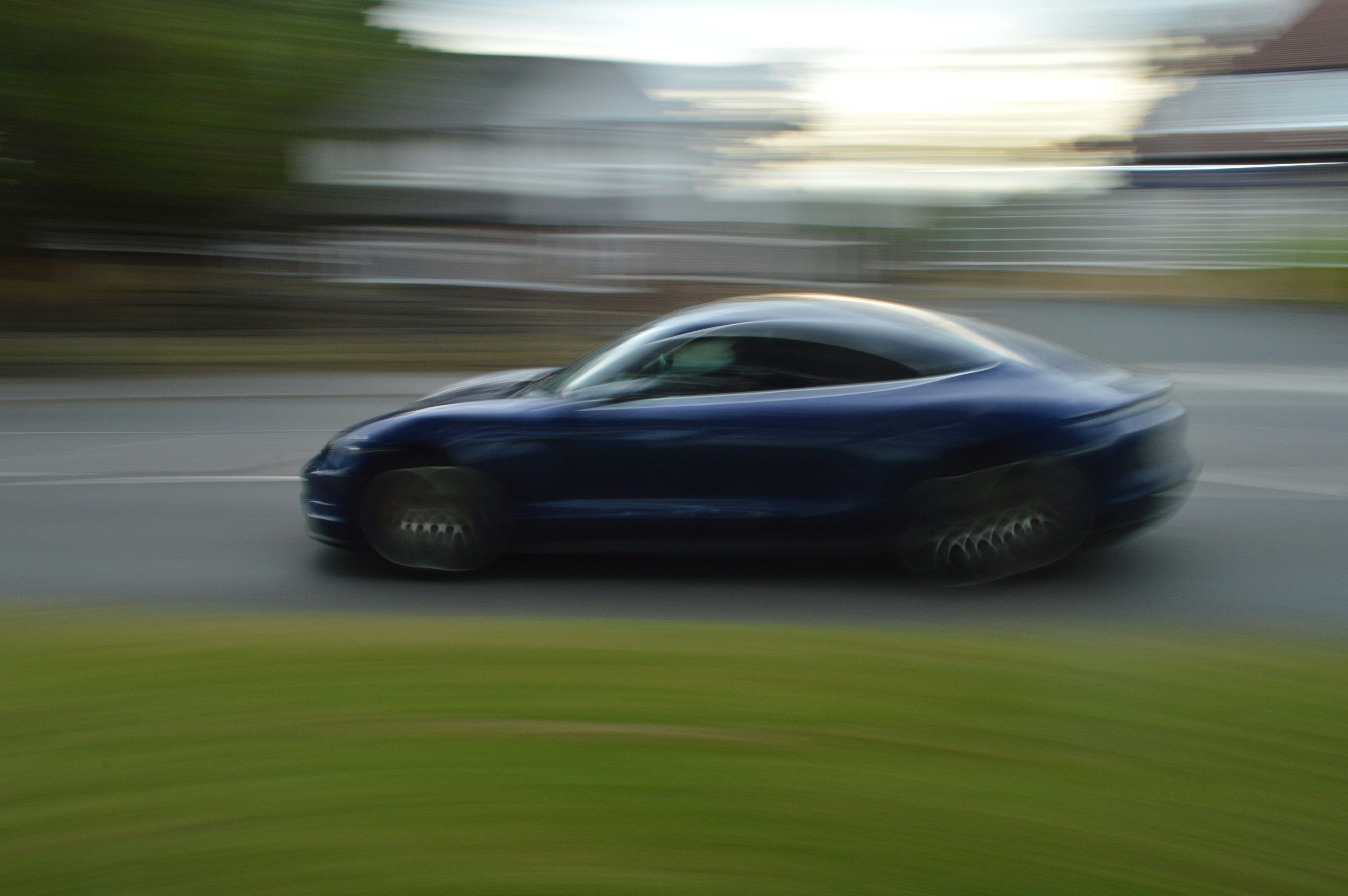 Blue coupe in motion blur along a suburban street