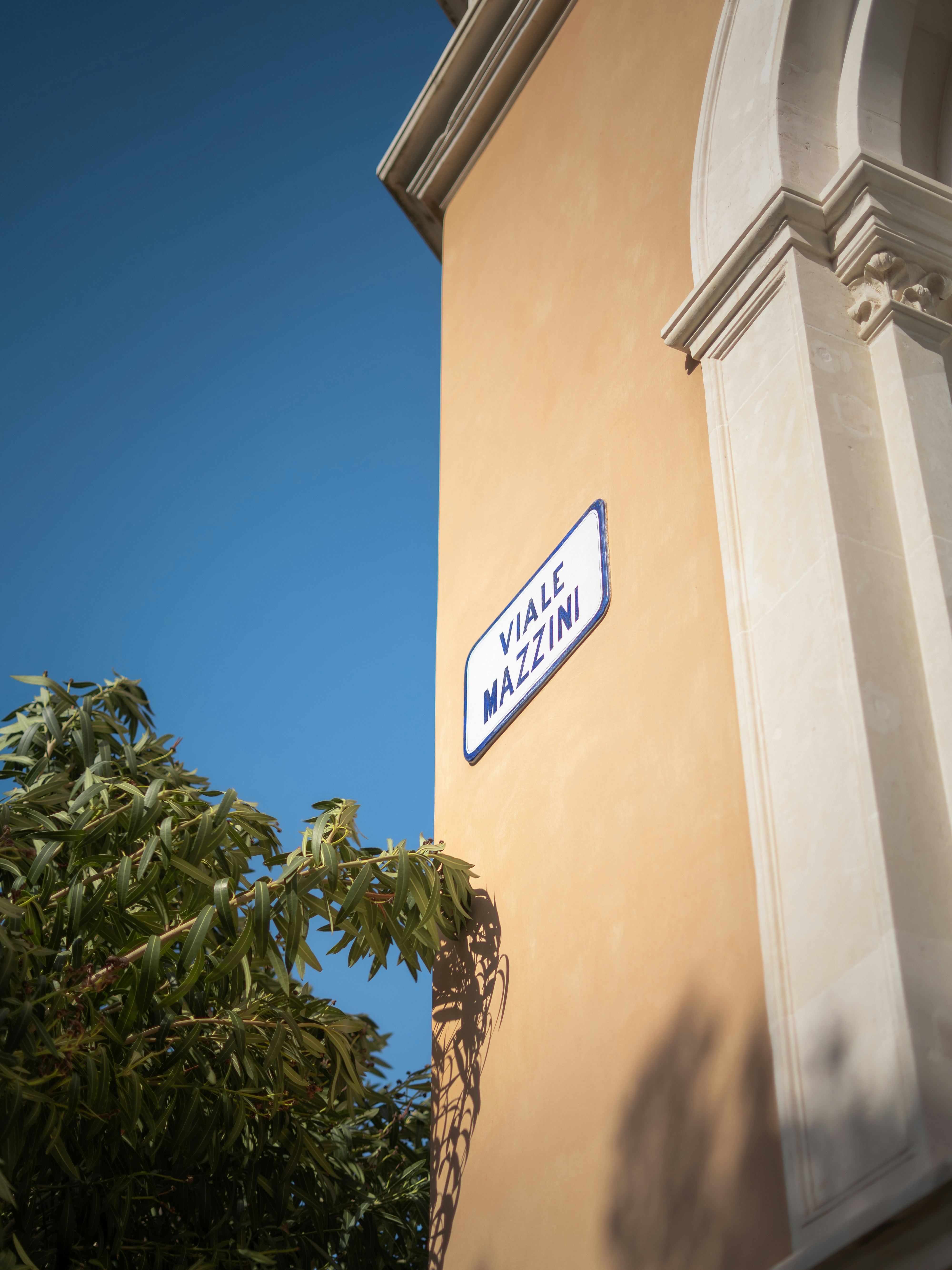 Vial of Mazini: A Sunlit Street Sign on Warm Facade