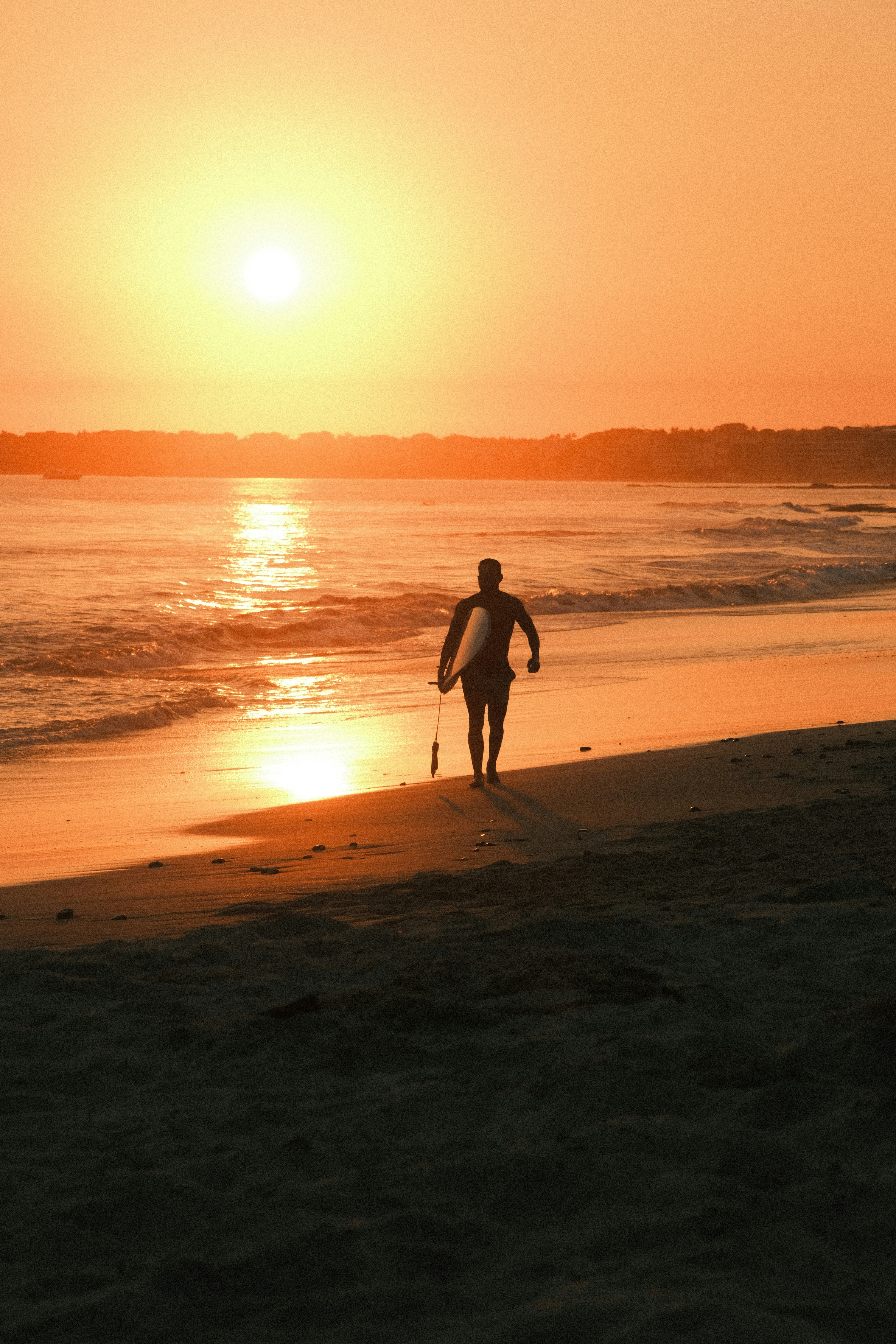 Sunset Stride: A solitary surfer walks the shoreline at golden hour
