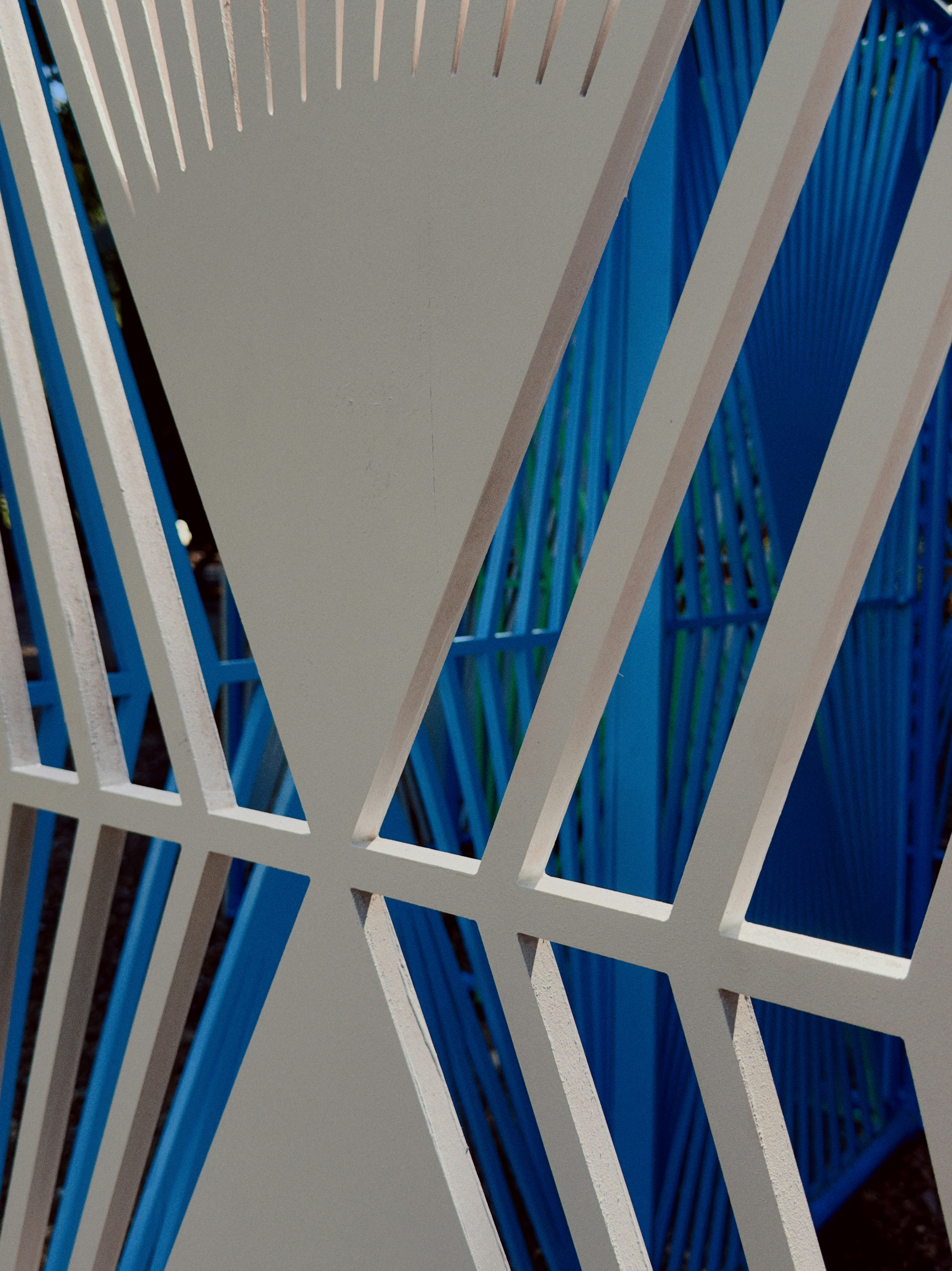 Abstract geometric framework of white slats forming angular patterns against blue vertical bars, creating a dynamic depth.