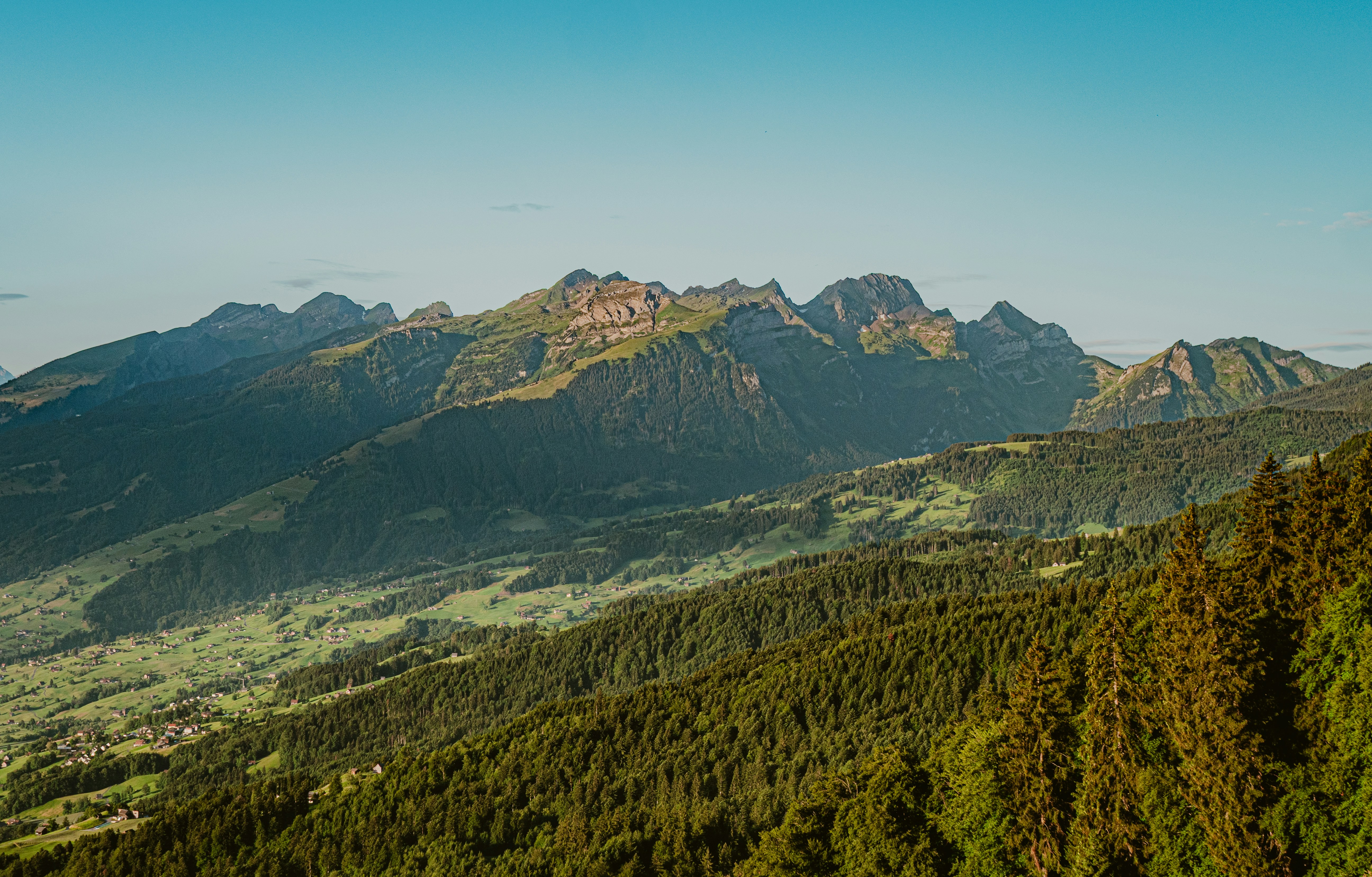 Majestic mountains and lush green forests under a clear sky.