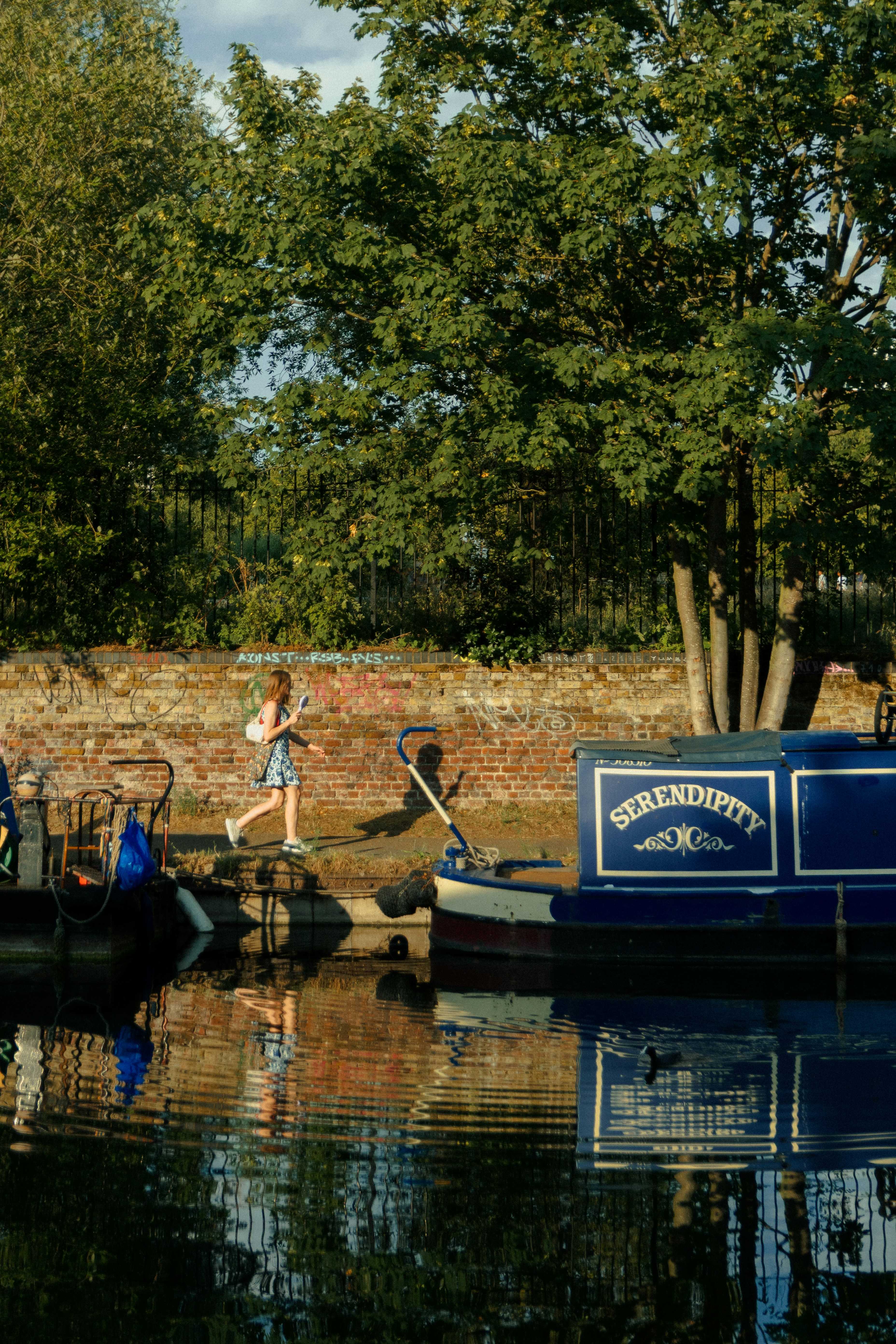 Stroll by the canal: a girl walks past the blue boat under dappled trees