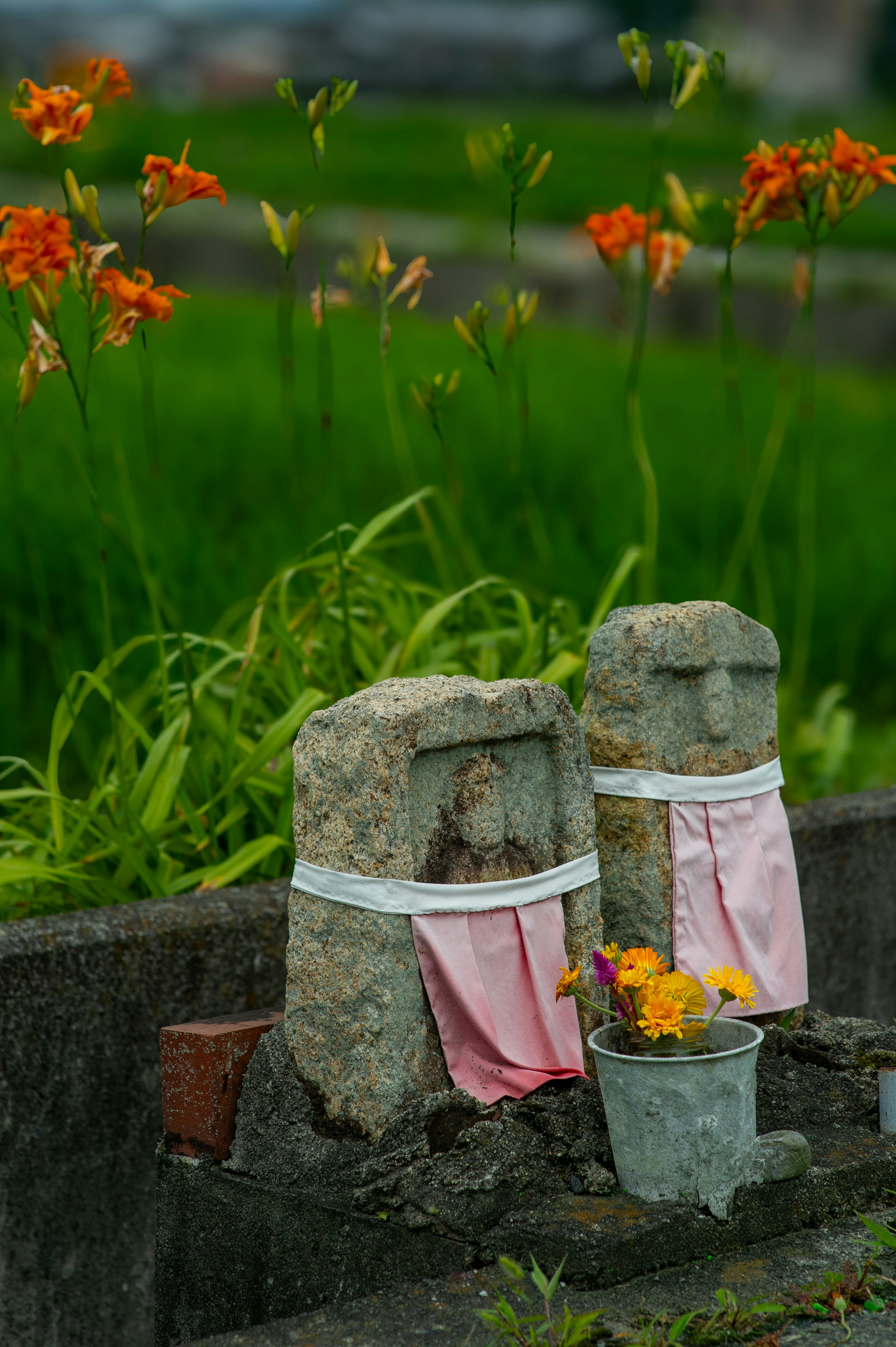 Weathered shrine guards a quiet garden with soft pink fabric and a metal cup of marigolds