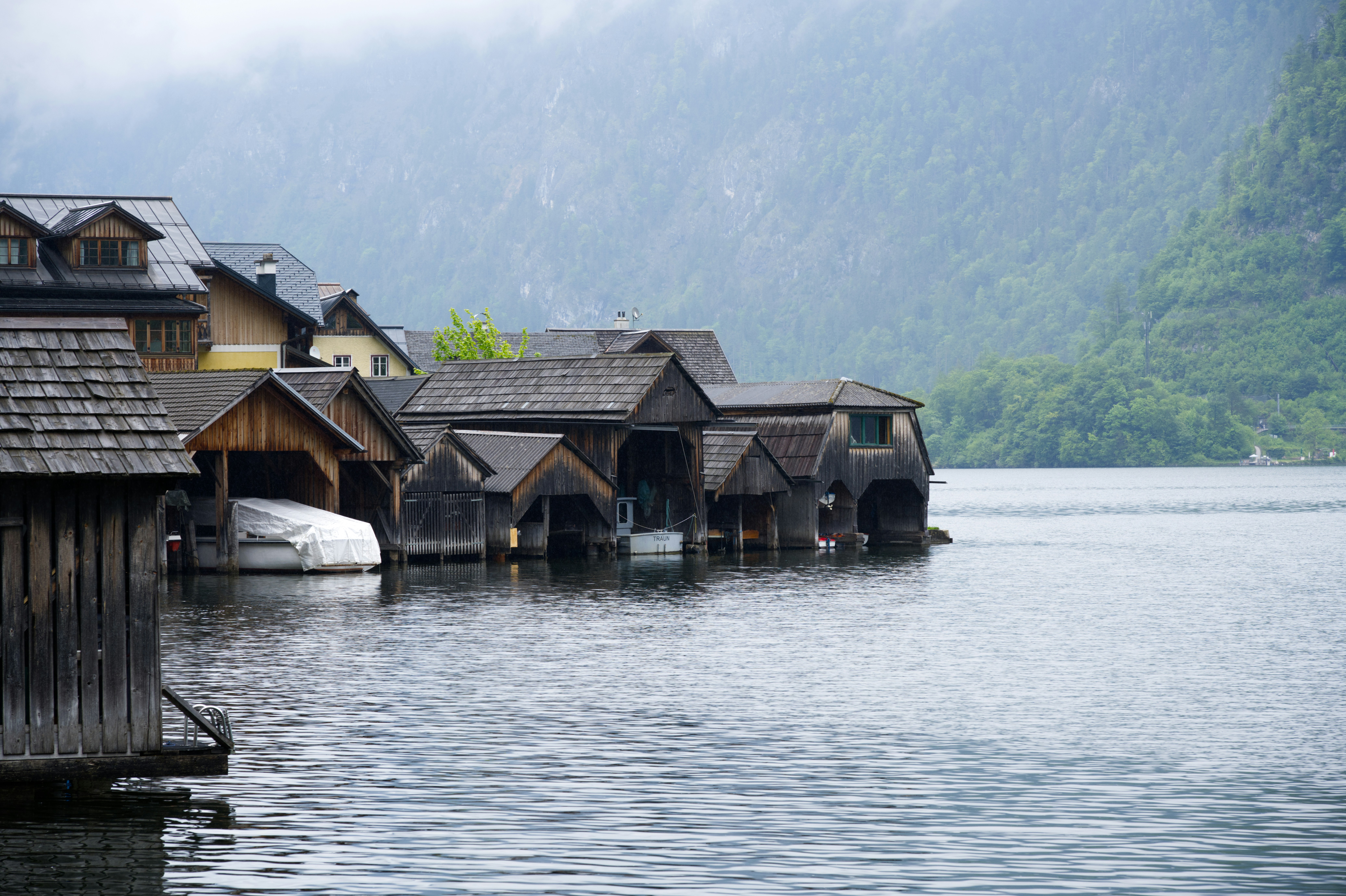 Sailboats Resting along Wooden Boathouses under Misty Mountains