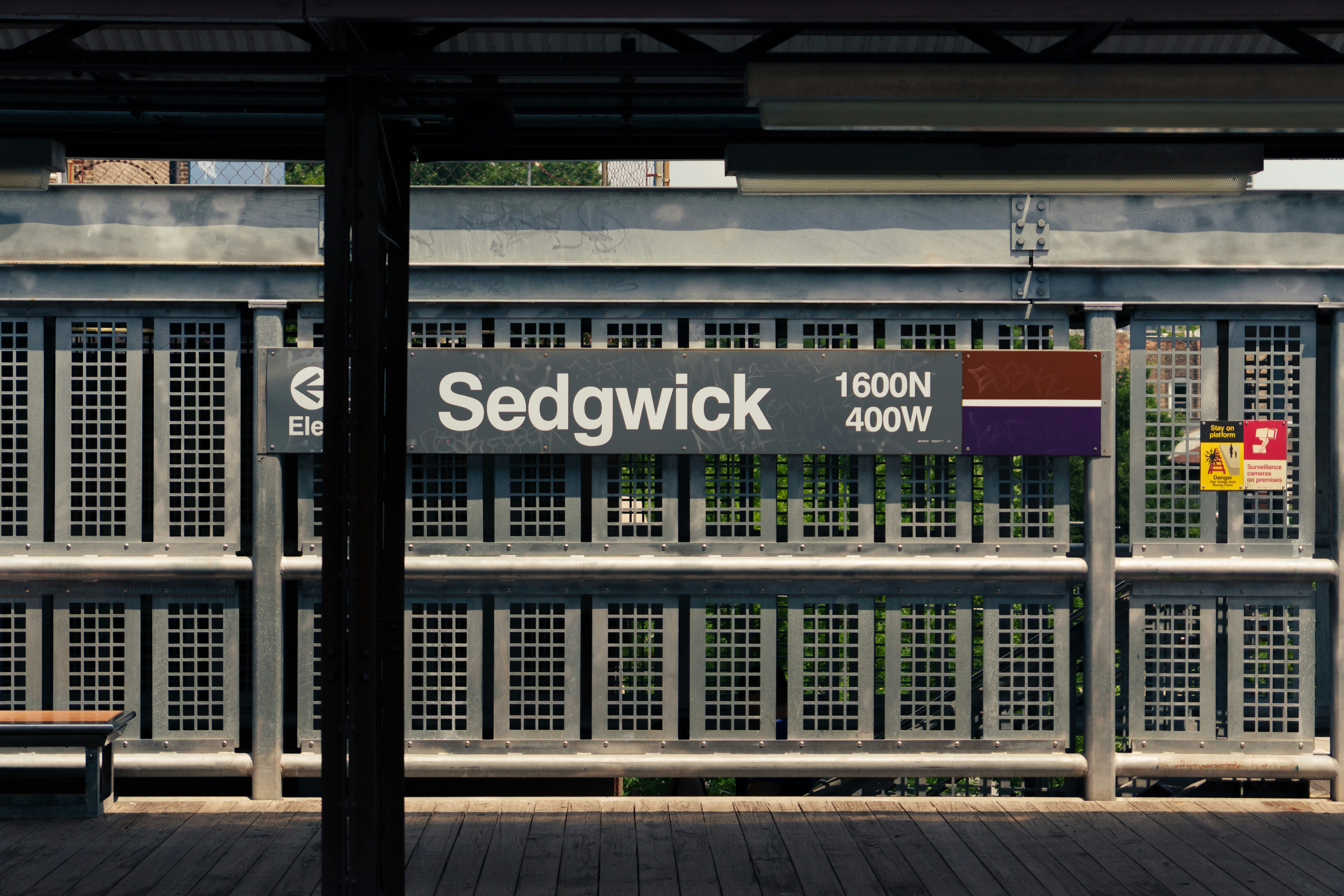 Platform signage at Sedgwick station framed by a metal grate, with structural beams and safety fencing in the background.