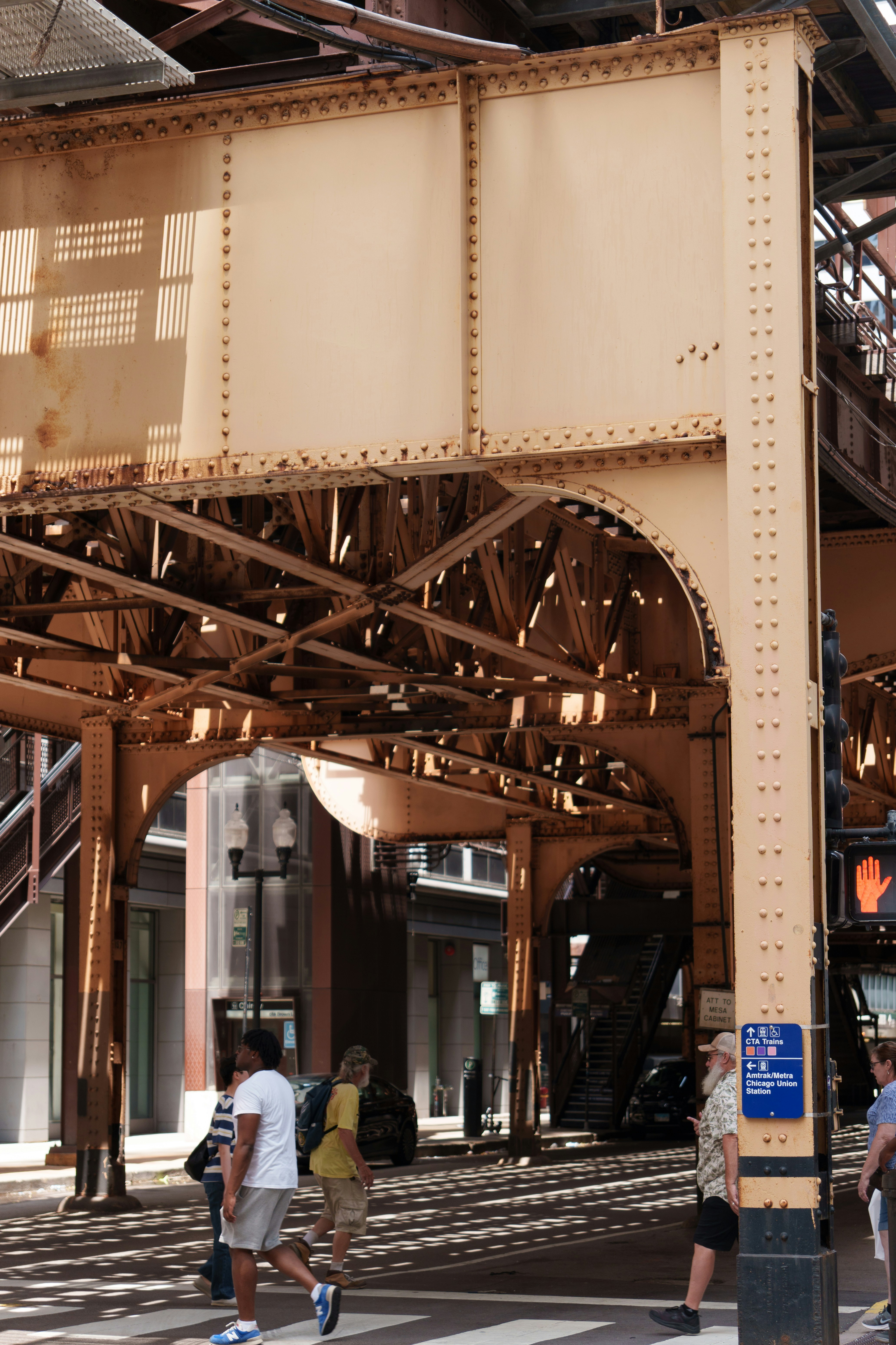 Rusted Steel Rhythm: Pedestrians Cross Beneath an Industrial Overpass