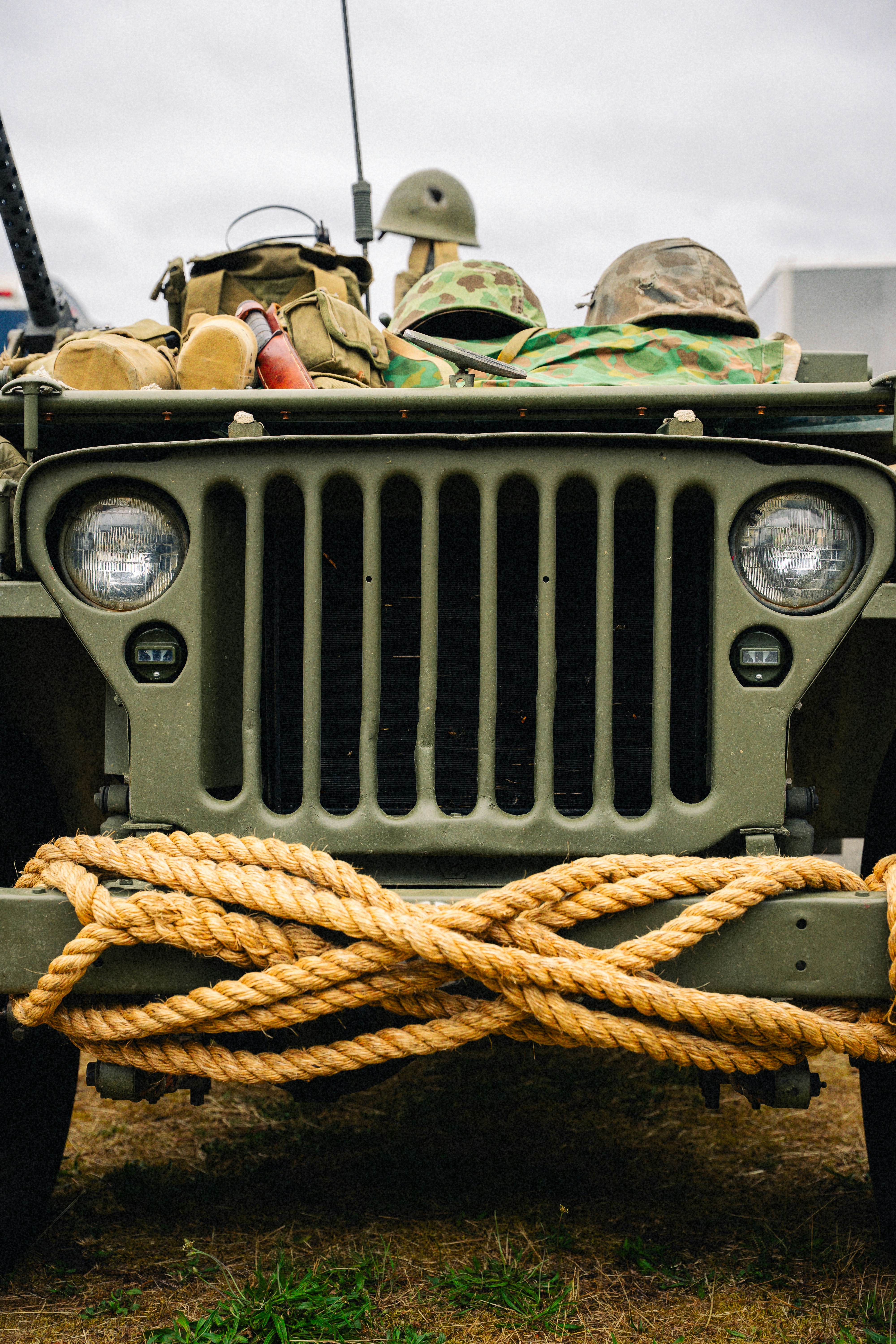 Military jeep with equipment stacked on the hood and a thick rope across the grille, ready for deployment.