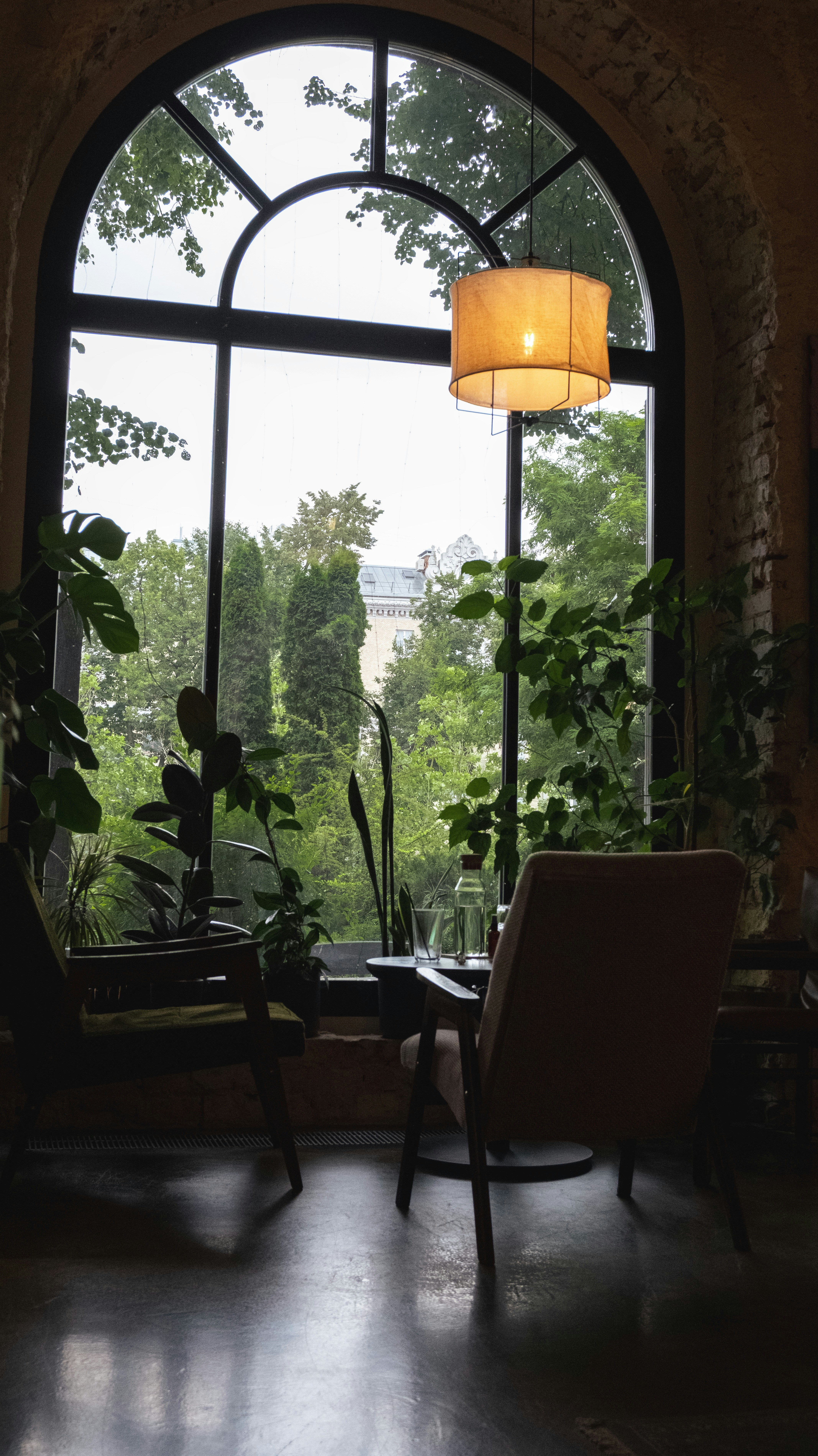 Indoor seating by a large arched window with lush plants and a warm pendant light, creating a tranquil cafe-like atmosphere.