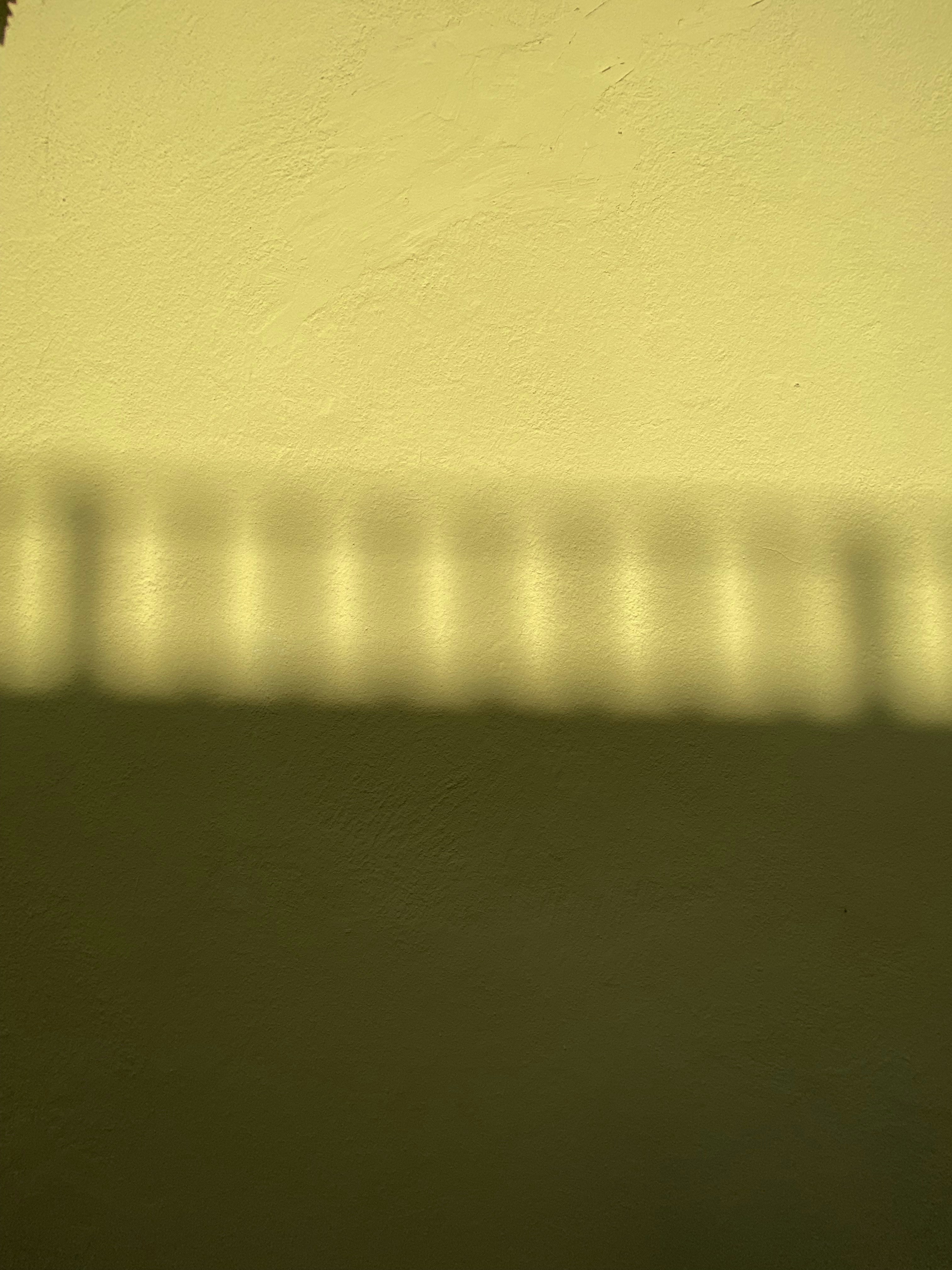Shadowed Balcony Rail, Blur on a Sunlit Yellow Wall