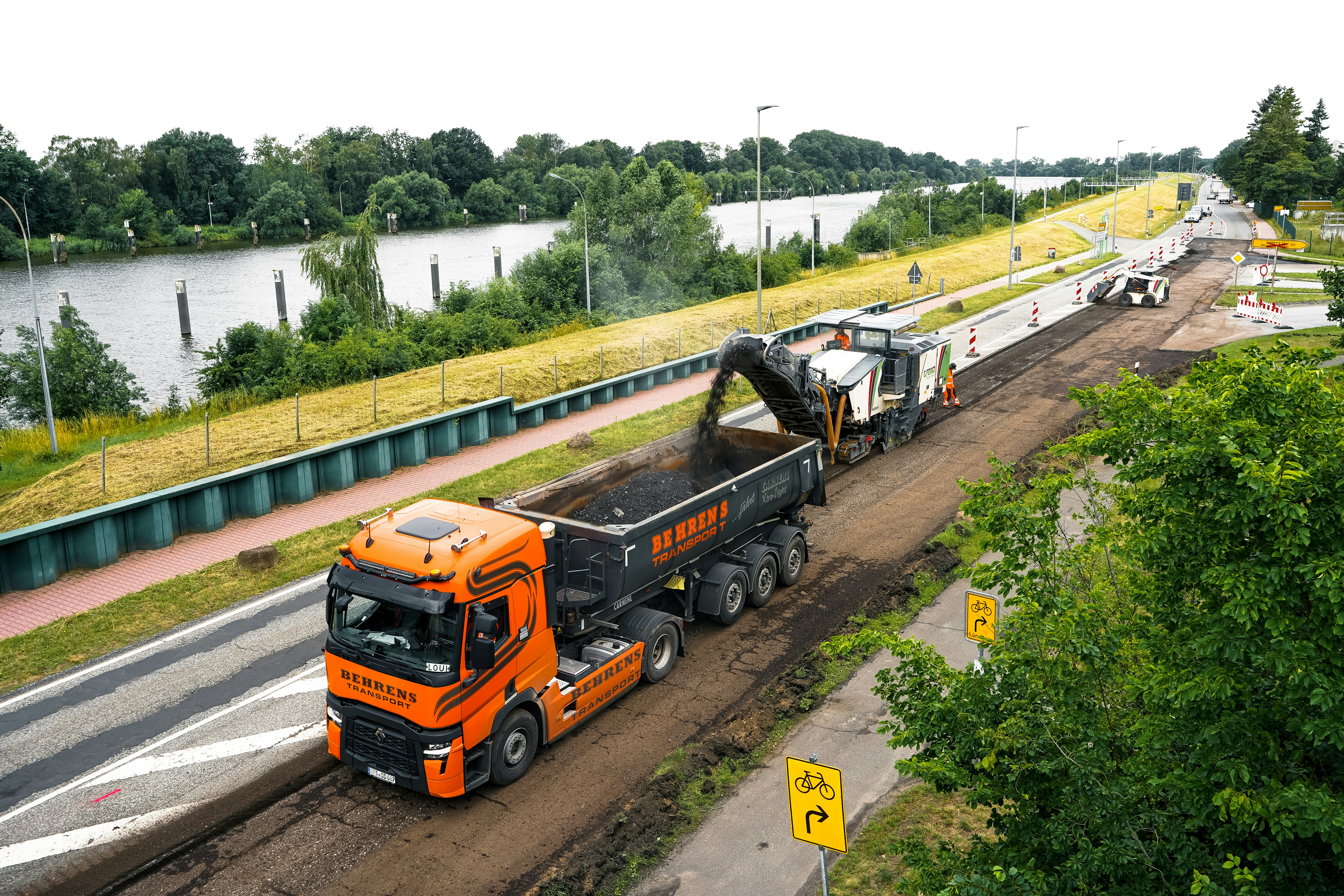 Orange Hauler Leads a Wake of Construction Toward a Riverbank