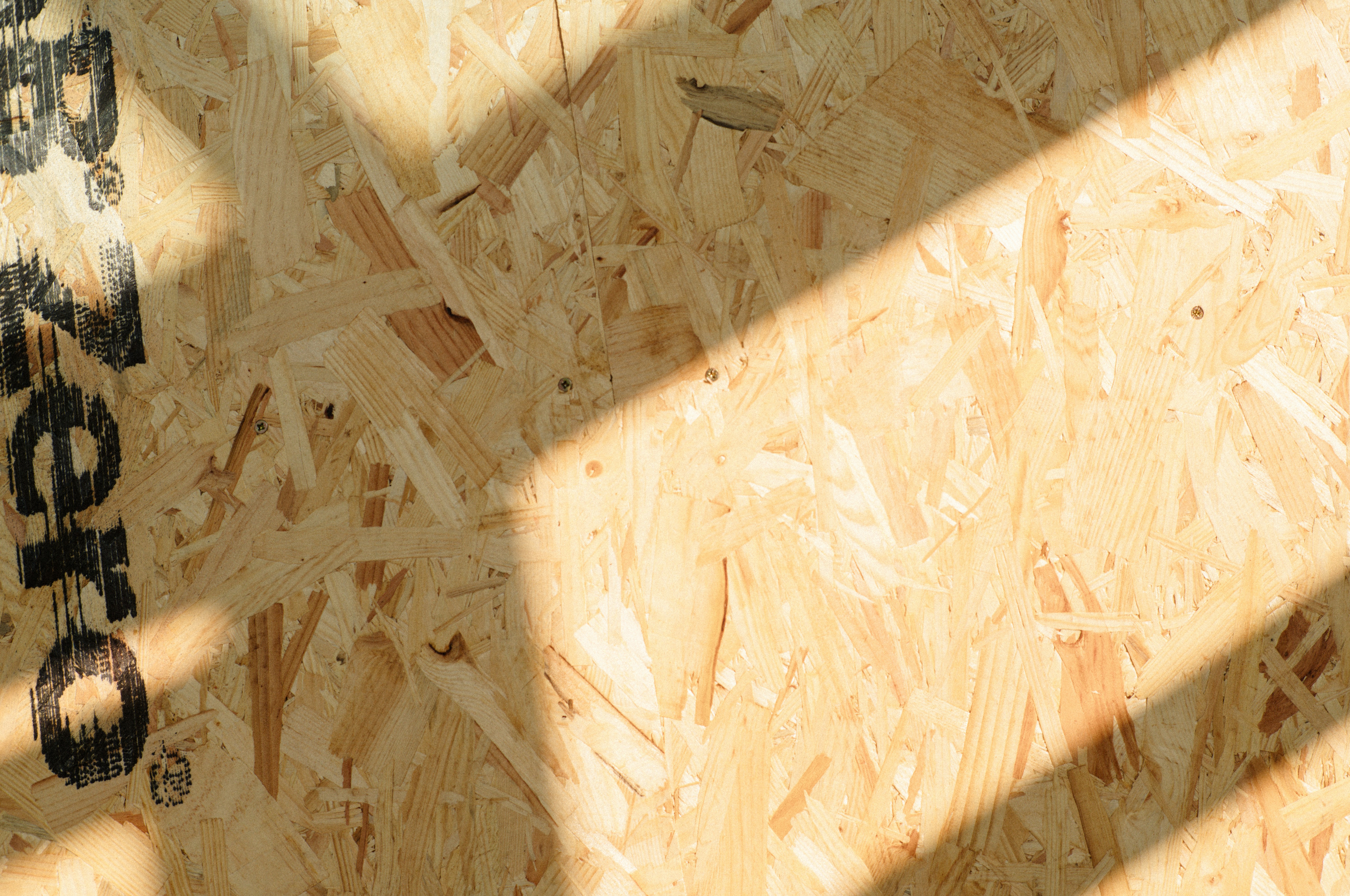 Sunlight carves angular shadows across textured OSB plywood, highlighting grain and surface imperfections without a human subject present.