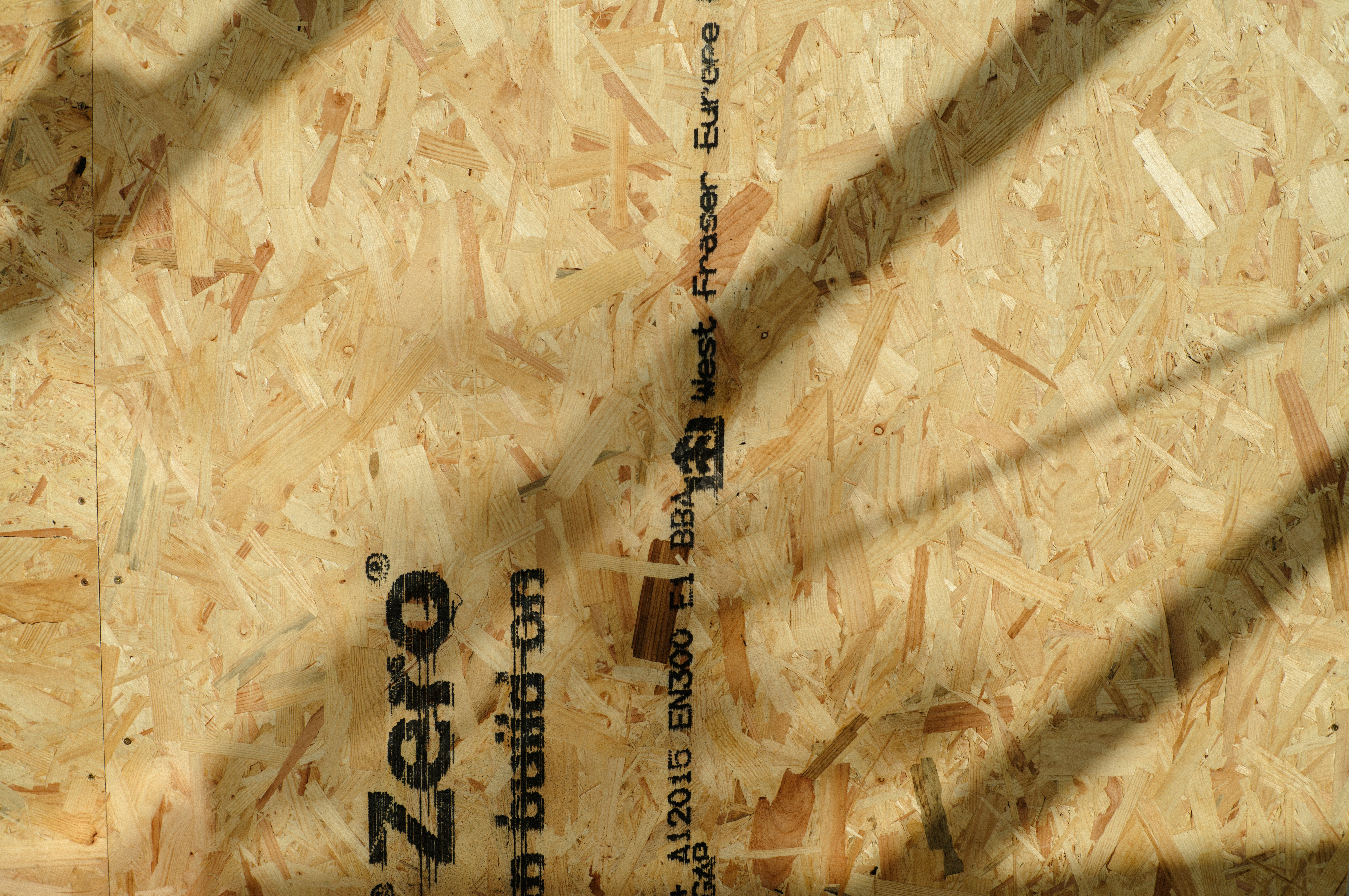 Close-up of oriented strand board with diagonal shadow lines creating abstract geometric patterns.