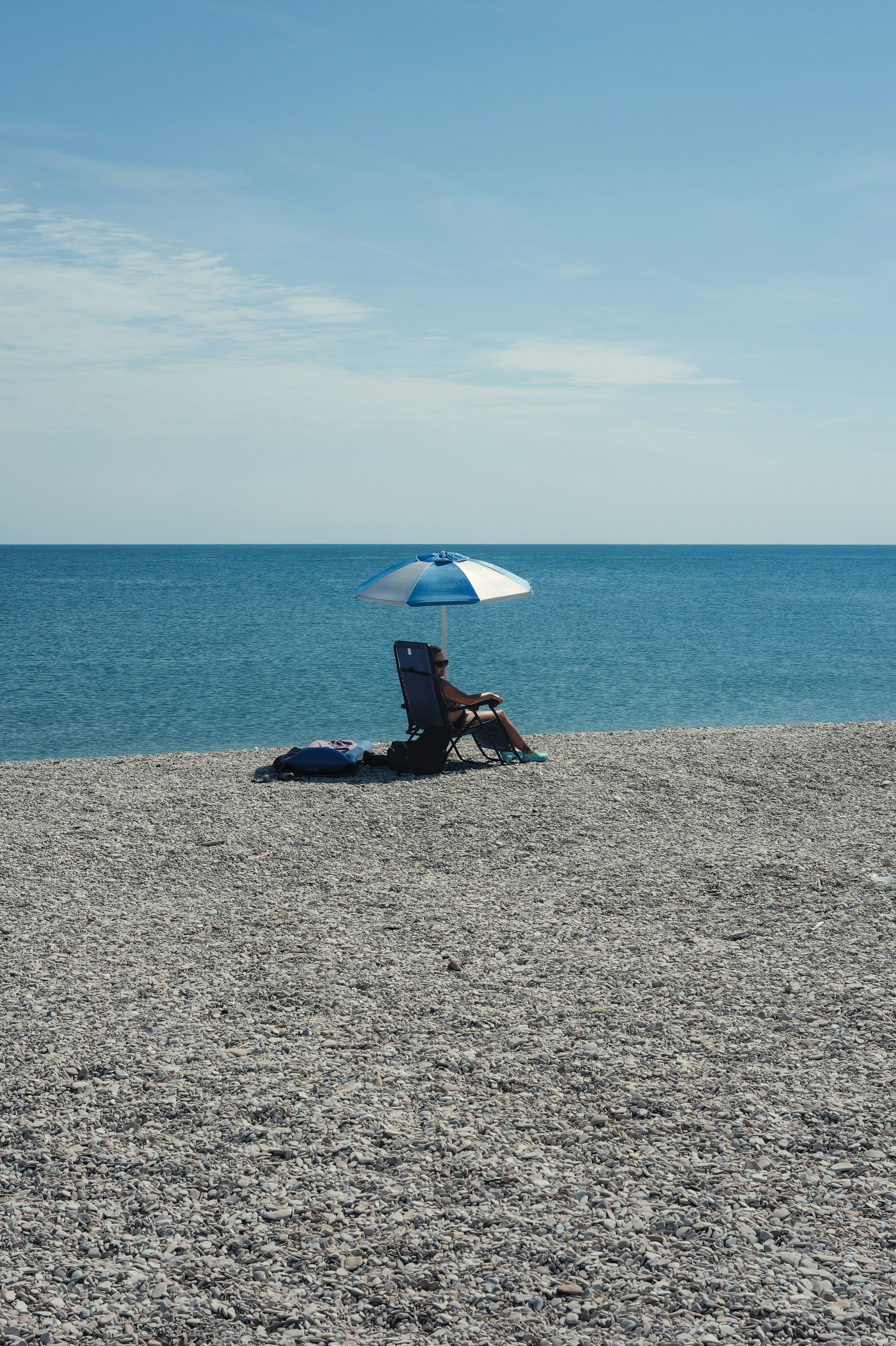 Solitude in the Sun: A Beachgoer Under a Dappled Umbrella
