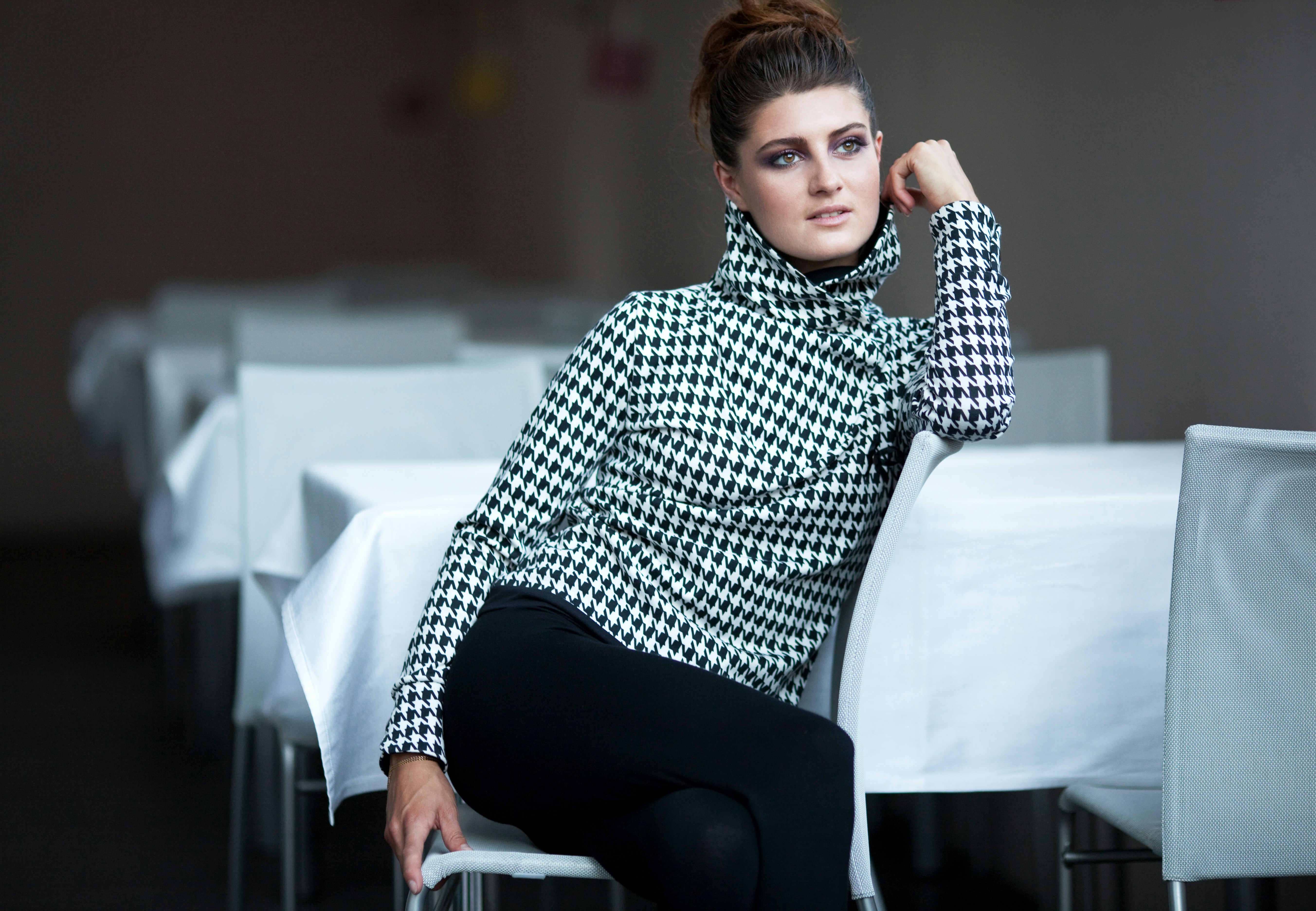 Chic Confidence: A Woman in a Houndstooth Turtleneck Reclines at a Minimalist Table