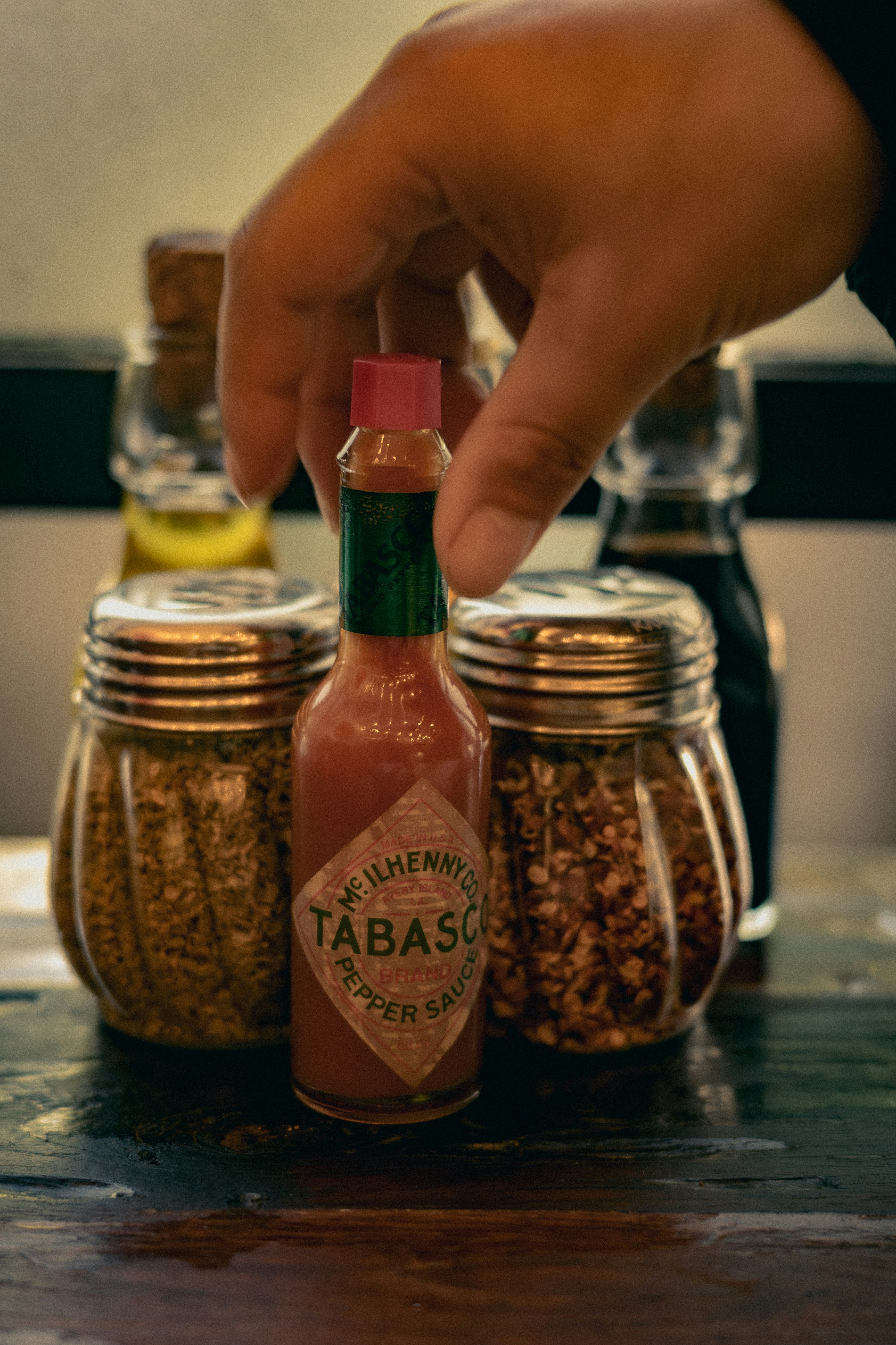 Hand picking up a small tabasco sauce bottle amidst spices.