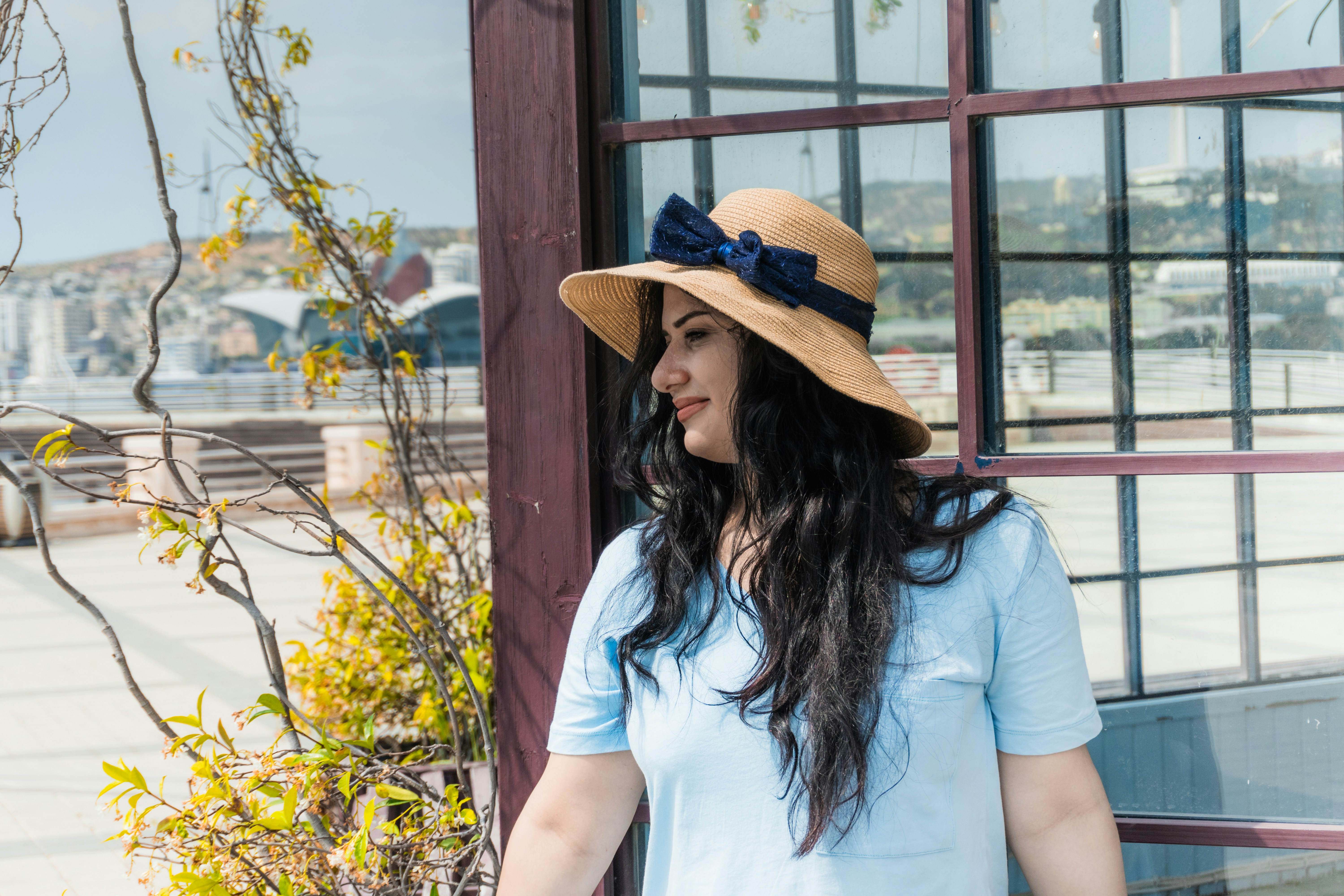 Sunlit hat and contemplative smile: a portrait on the rooftop veranda