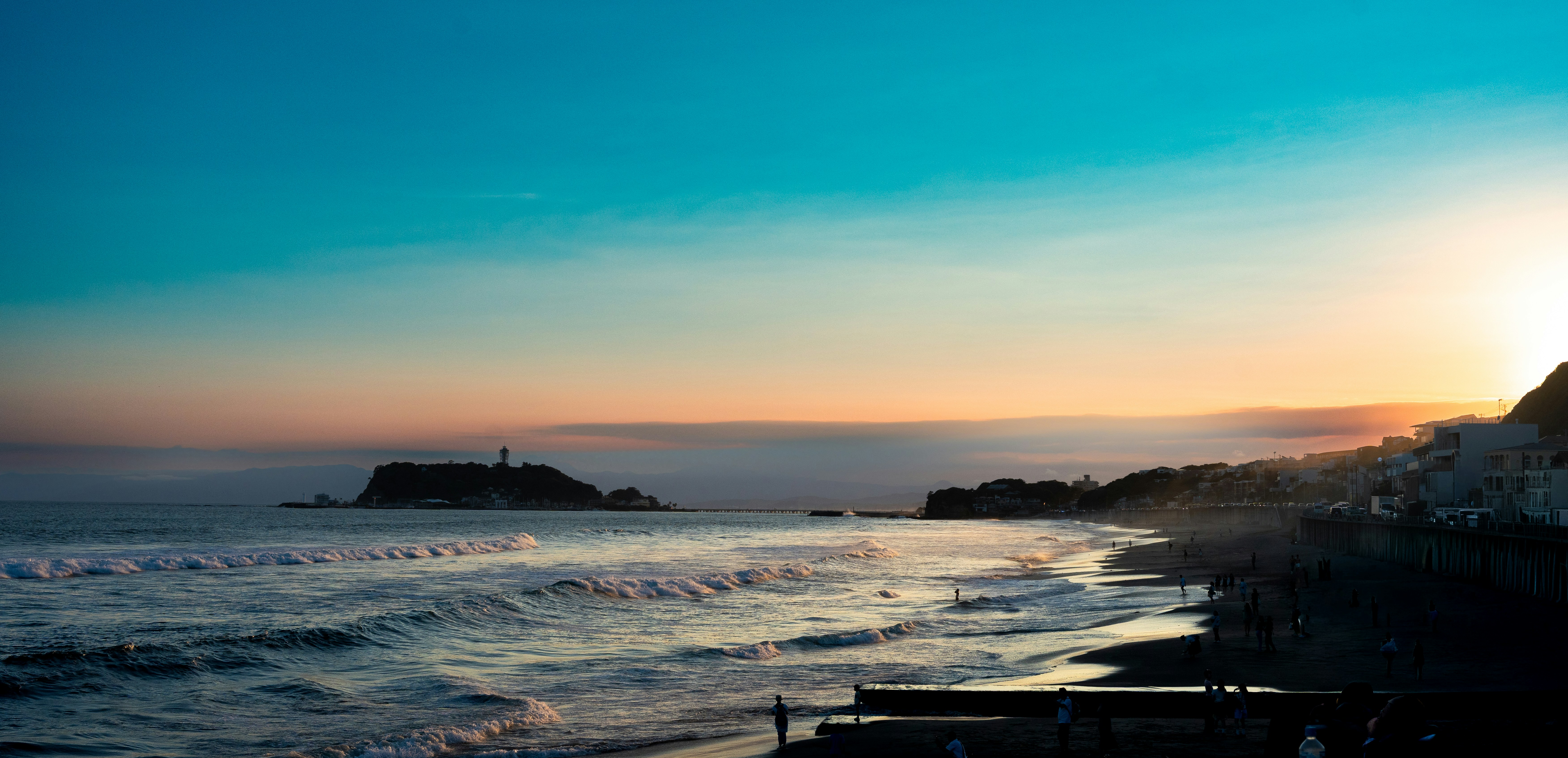 Dusk over a calm coastal scene with gentle waves and a distant headland under a gradient sky.