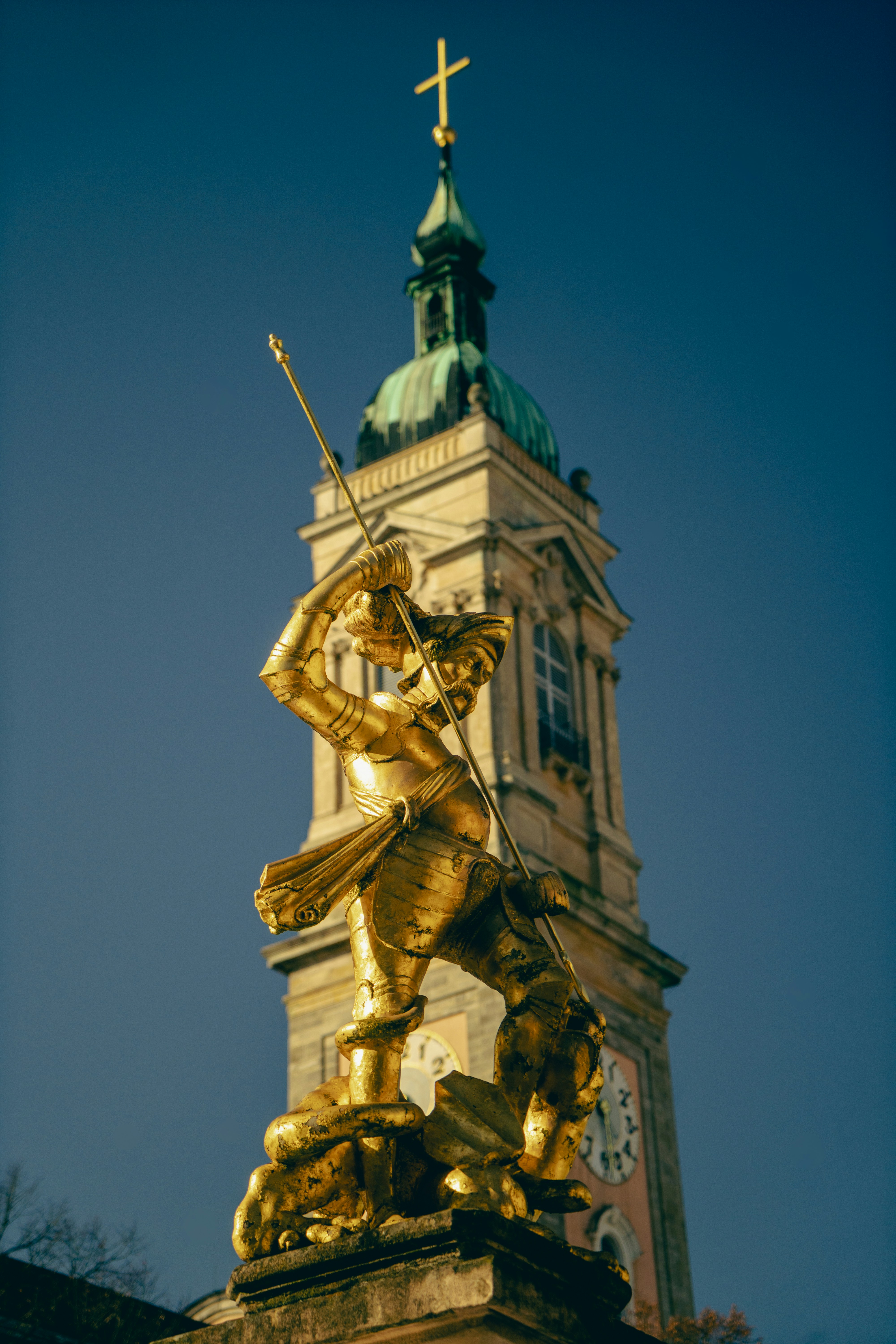 Golden Warrior and ancient spire: a statue in front of a clock tower at dusk