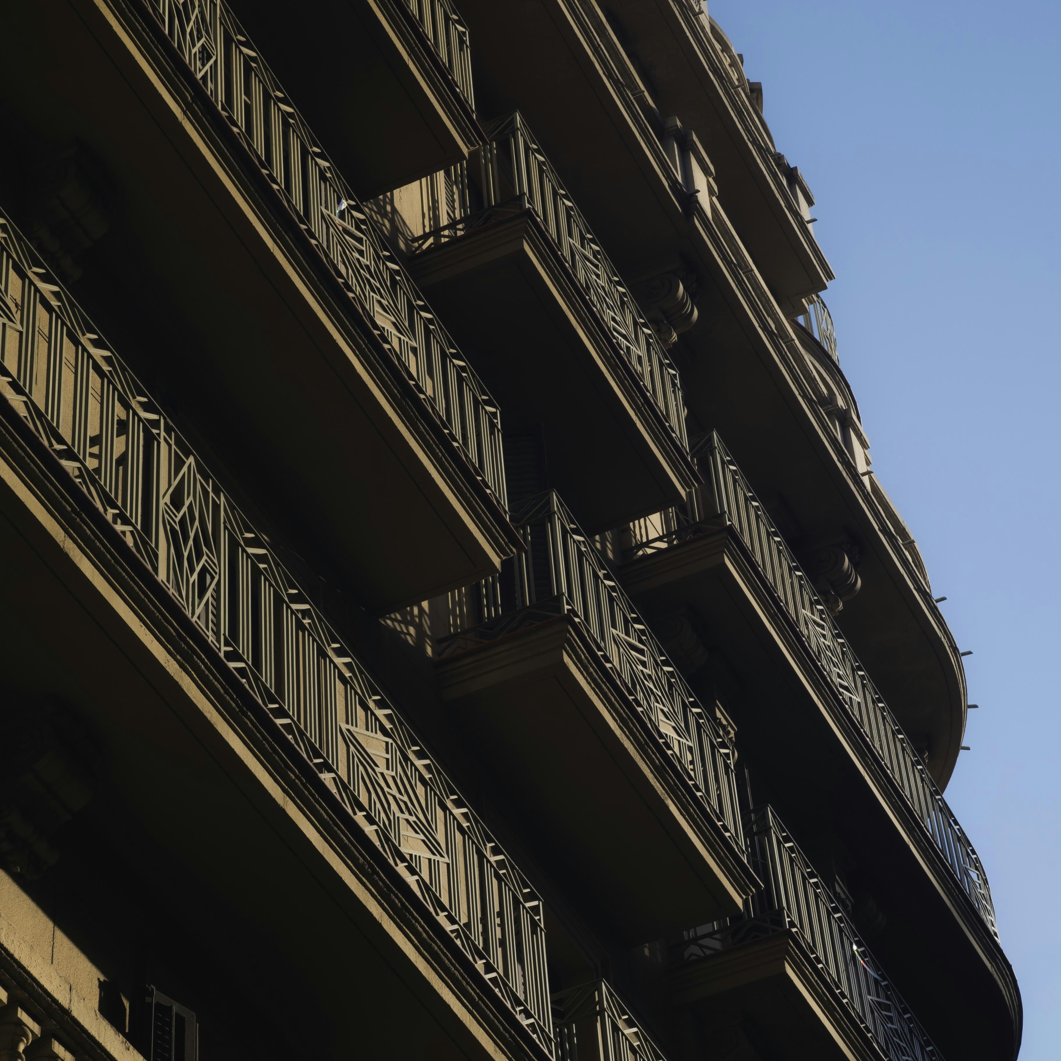 Diagonal view of a multi-story building with ornate balconies, bathed in late-day light against a clear blue sky. A architectural detail shot emphasizing repeating railings and shadows.