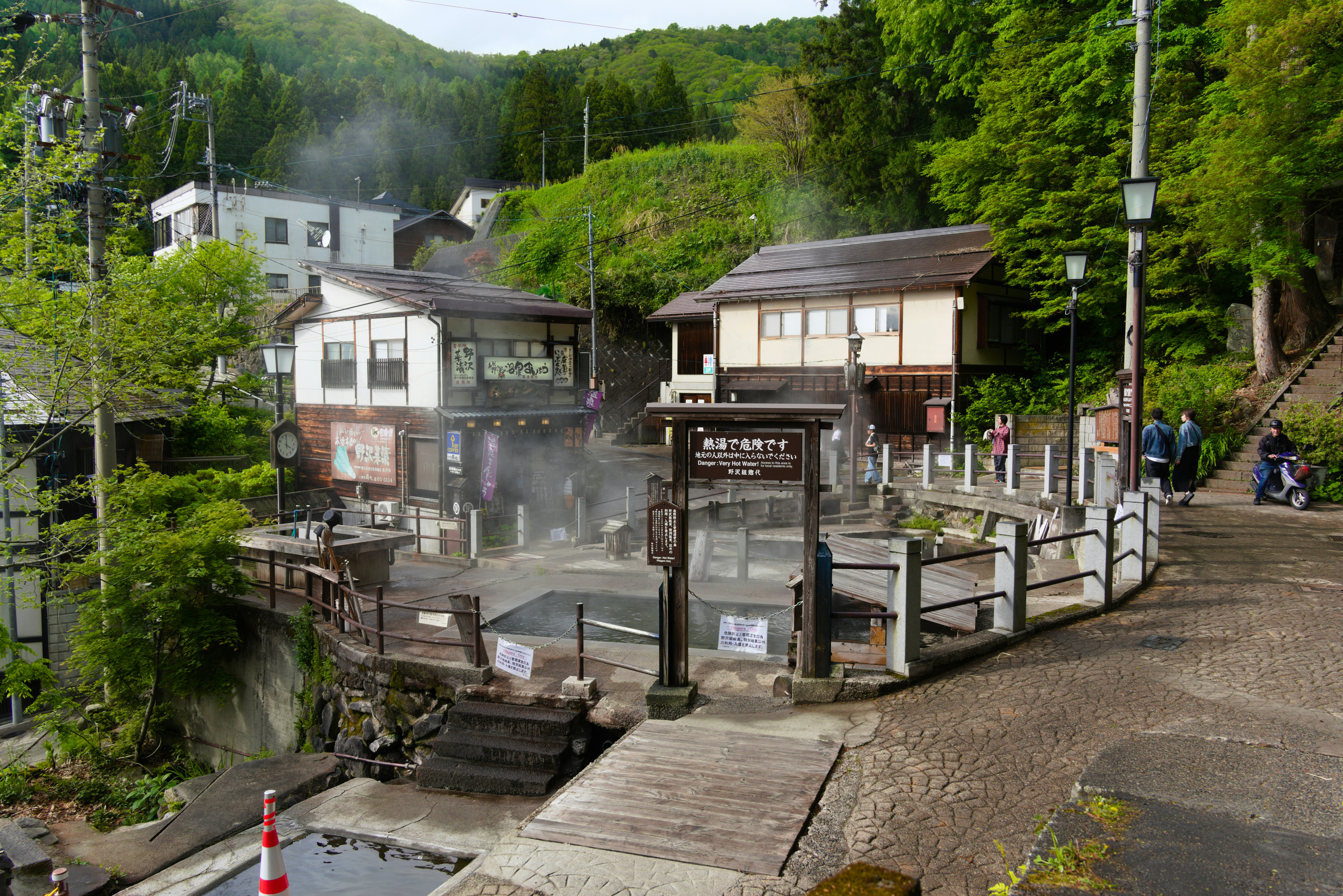 Steam-Speckled Onsen Village at the Base of a Lush Green Hill