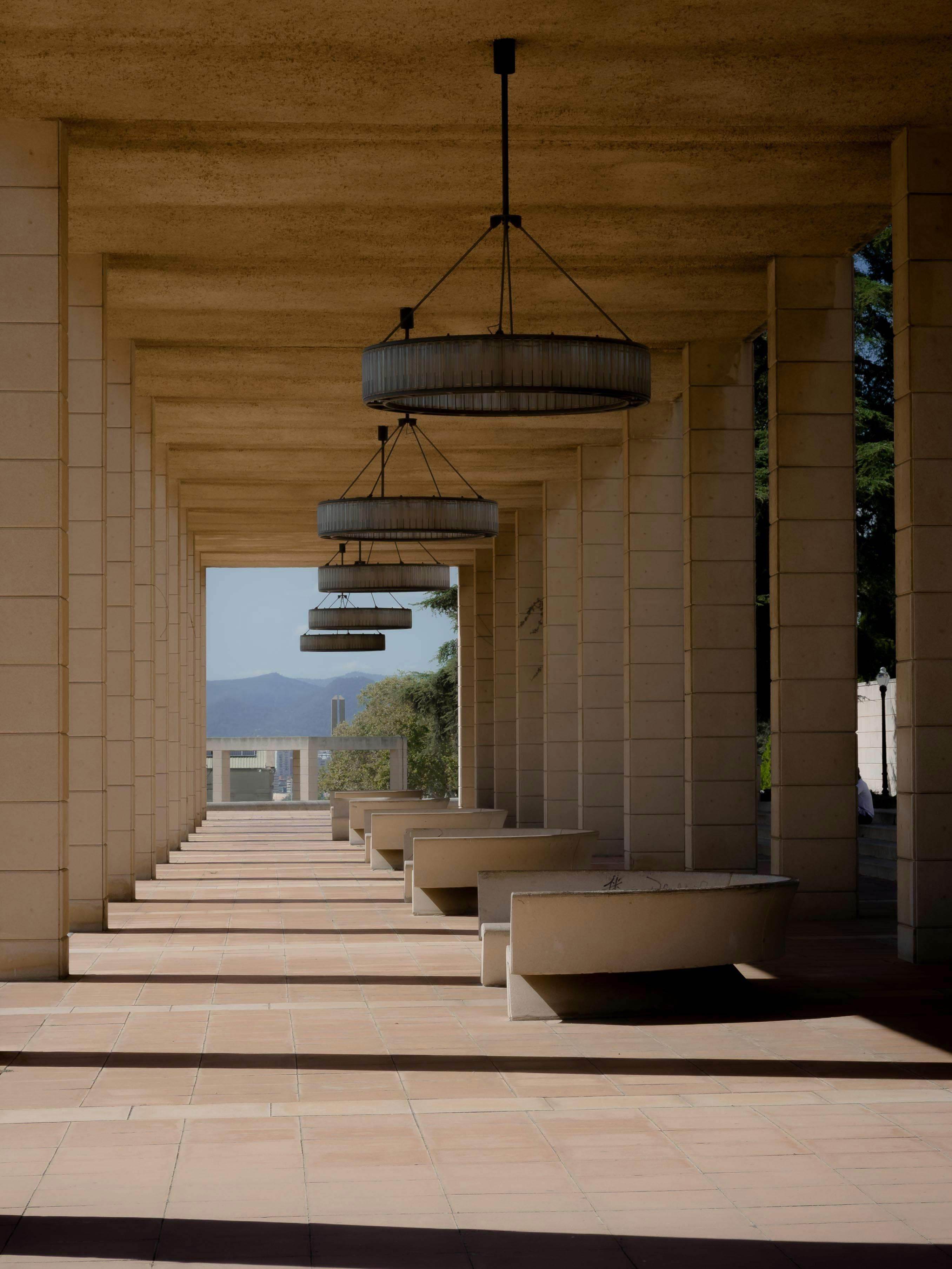 Long colonnade with geometric shadows and hanging circular light fixtures receding into the distance; architectural scene emphasizing perspective. (photograph) The image is a captured architectural photography.