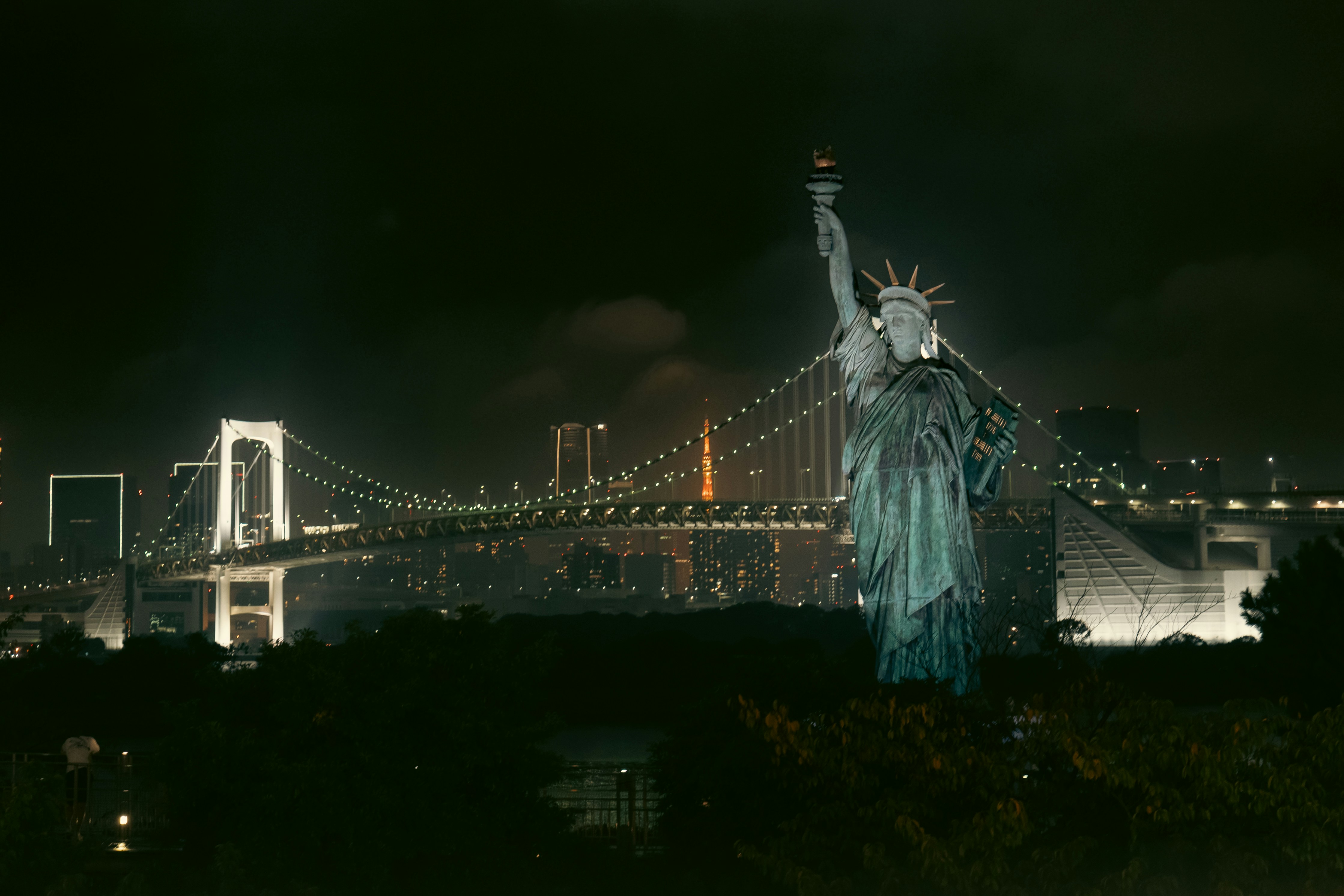 Statue of Liberty over Tokyo skyline at night with illuminated bridge