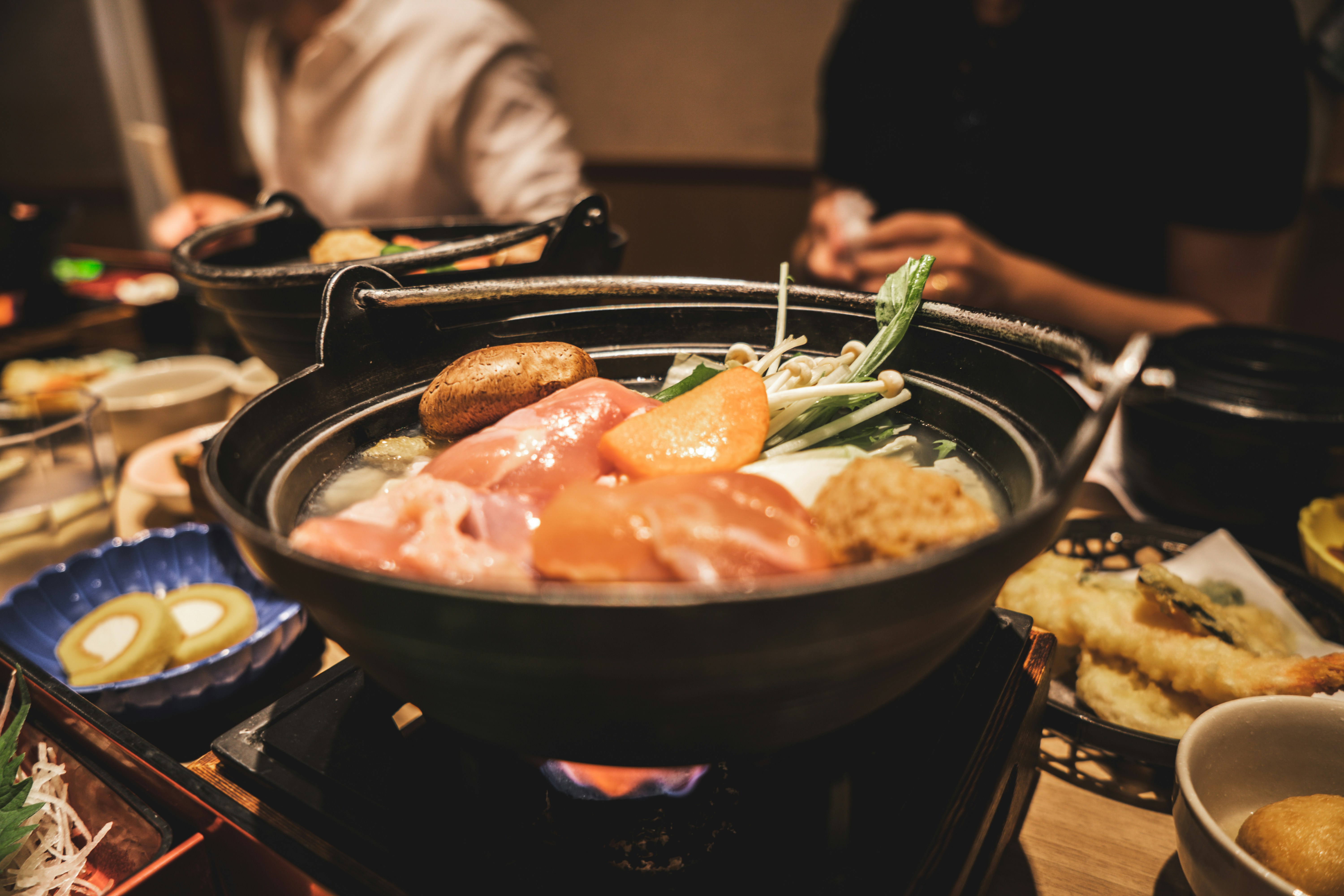 Steaming communal pot: thinly sliced meat and greens simmering at a lively table