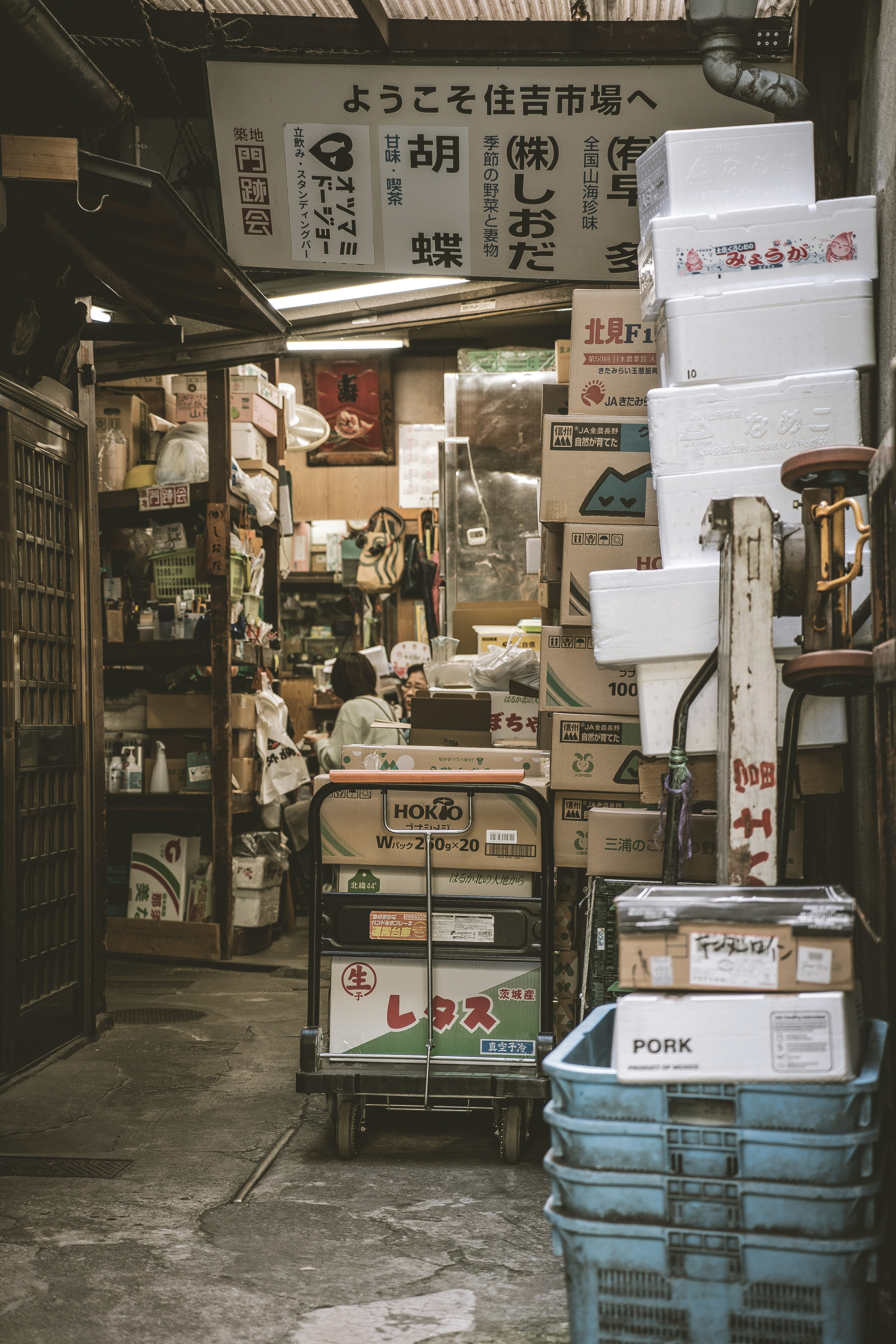Cluttered alleyway entrance with stacked boxes and a hand truck.
