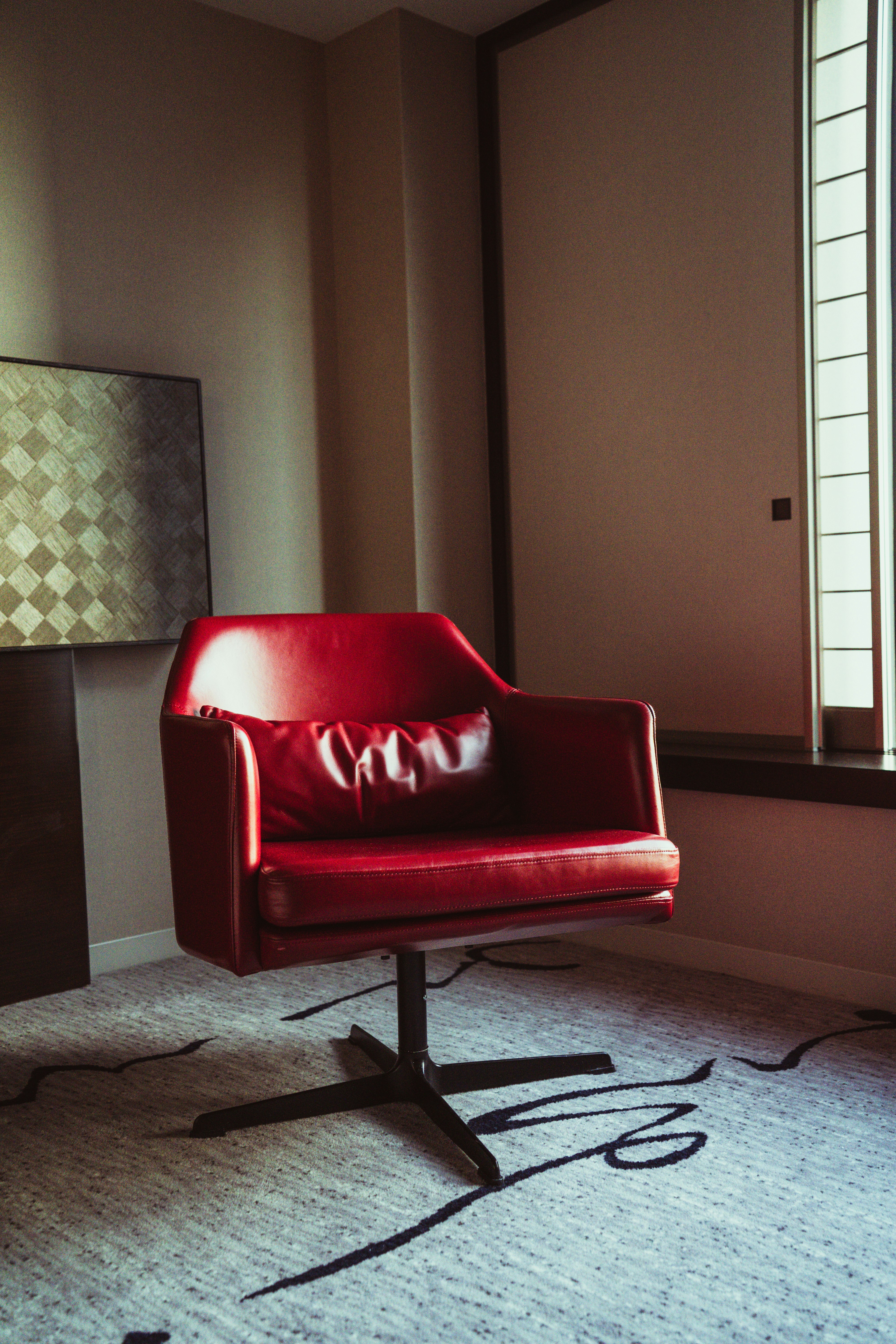 Red Accent: A lone chair in a sunlit hotel corner
