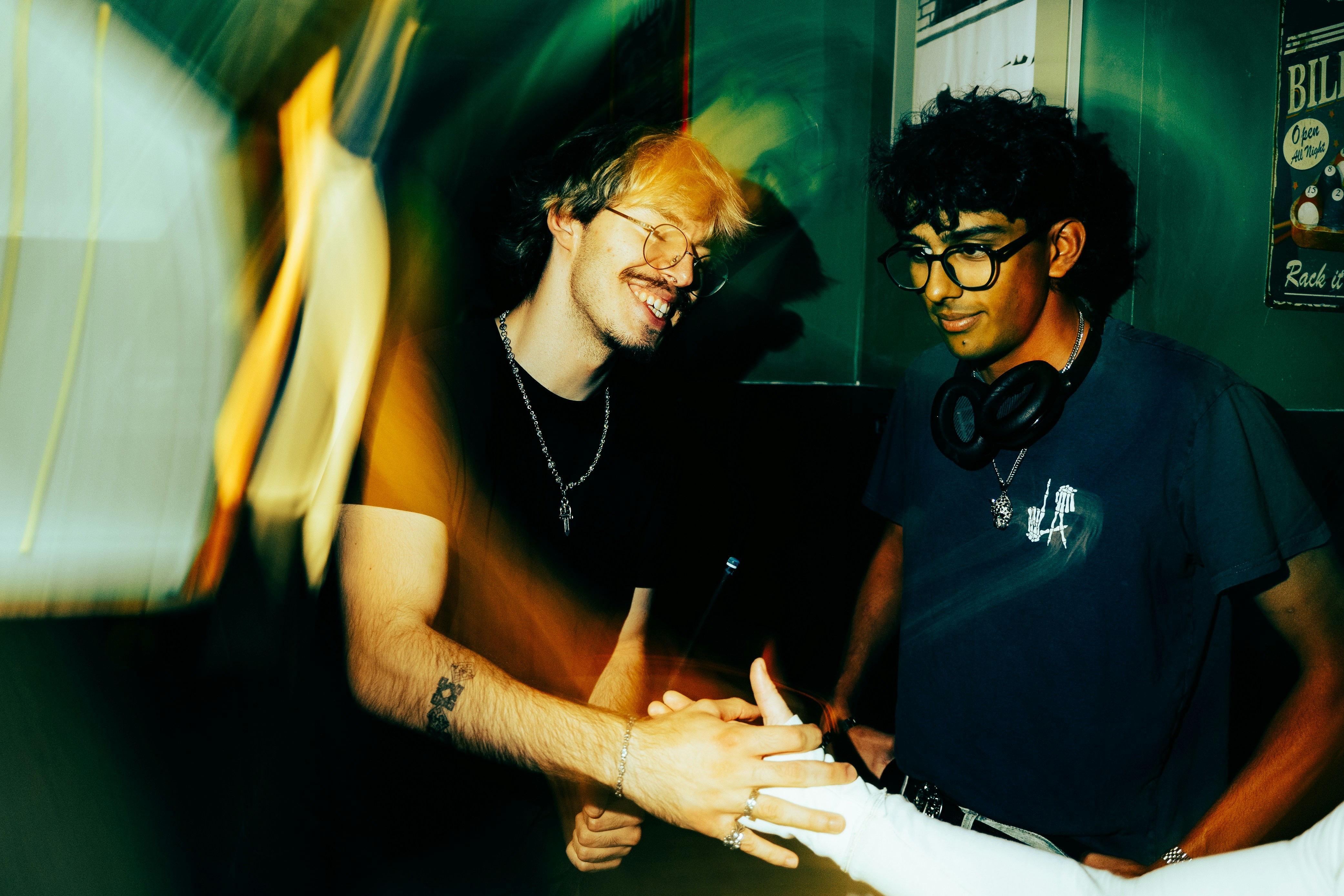 Two friends vibing backstage: neon green walls and motion blur feathering around a shared moment