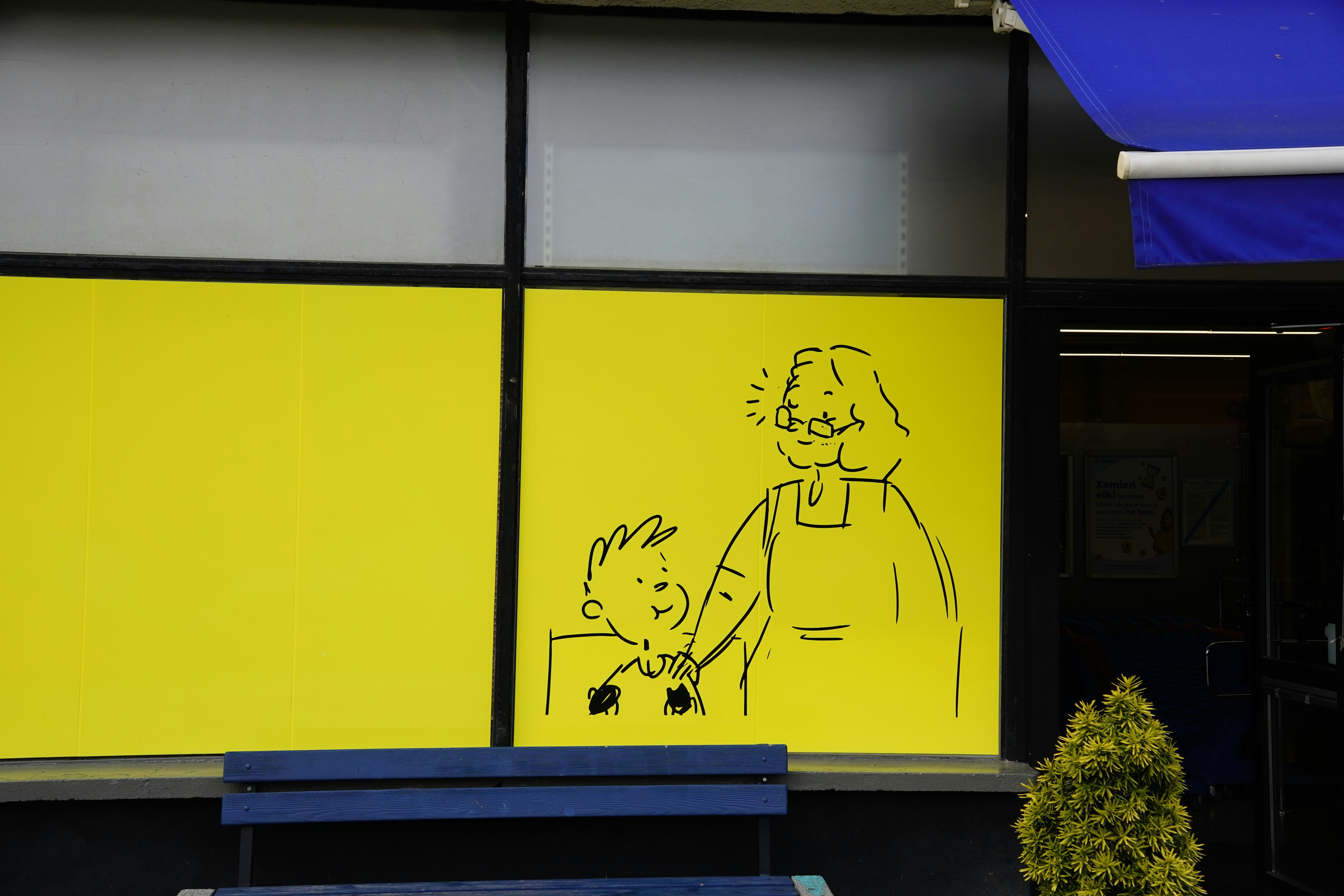 Yellow storefront window with chalky cartoon figures beside a bench