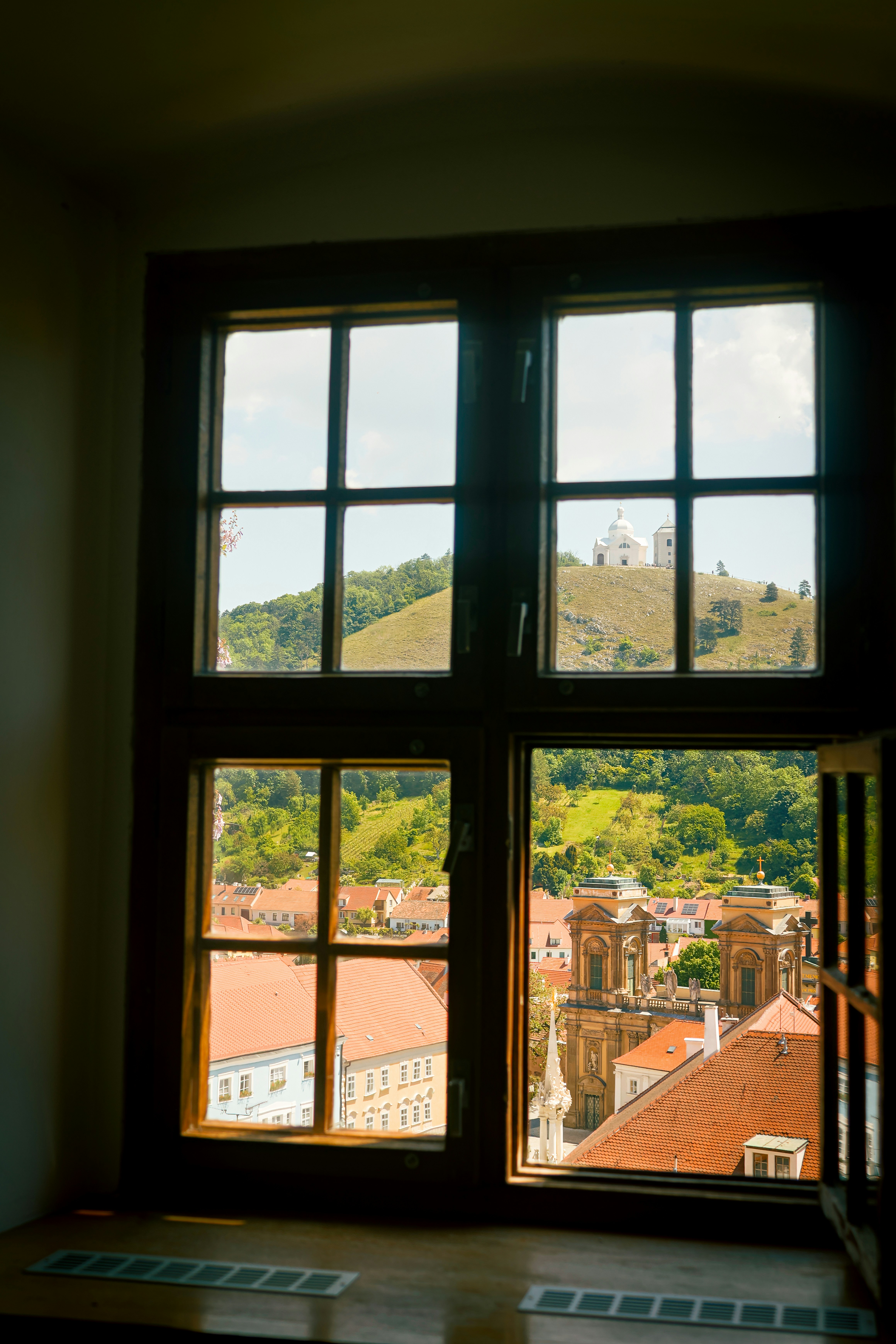 View Through Old Window: Hilltop Chapel and Red-Tiled Cityscape