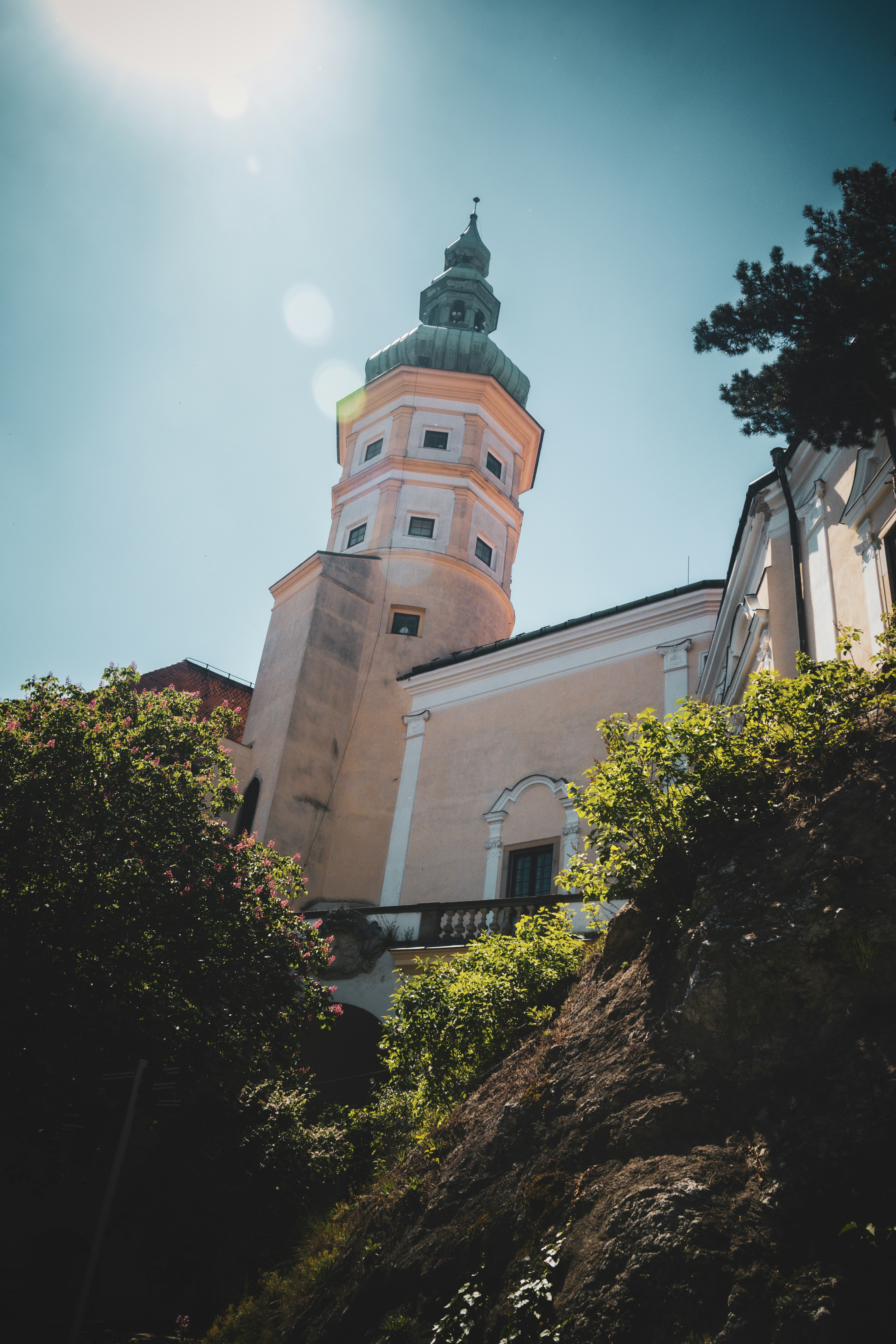 Clocktower rises over sunlit courtyard, framed by lush greenery