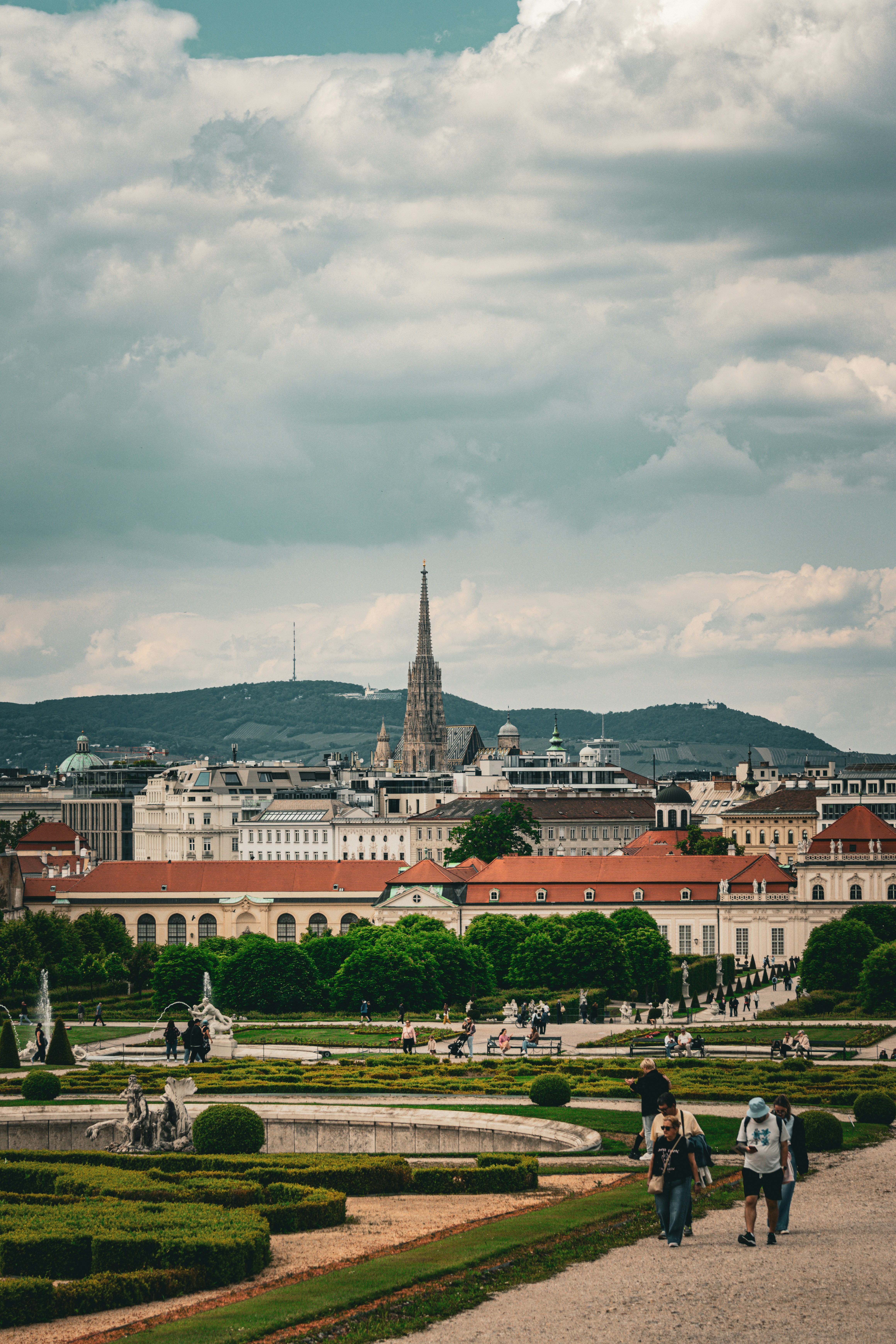 City skyline with spire and formal gardens beneath a dramatic sky