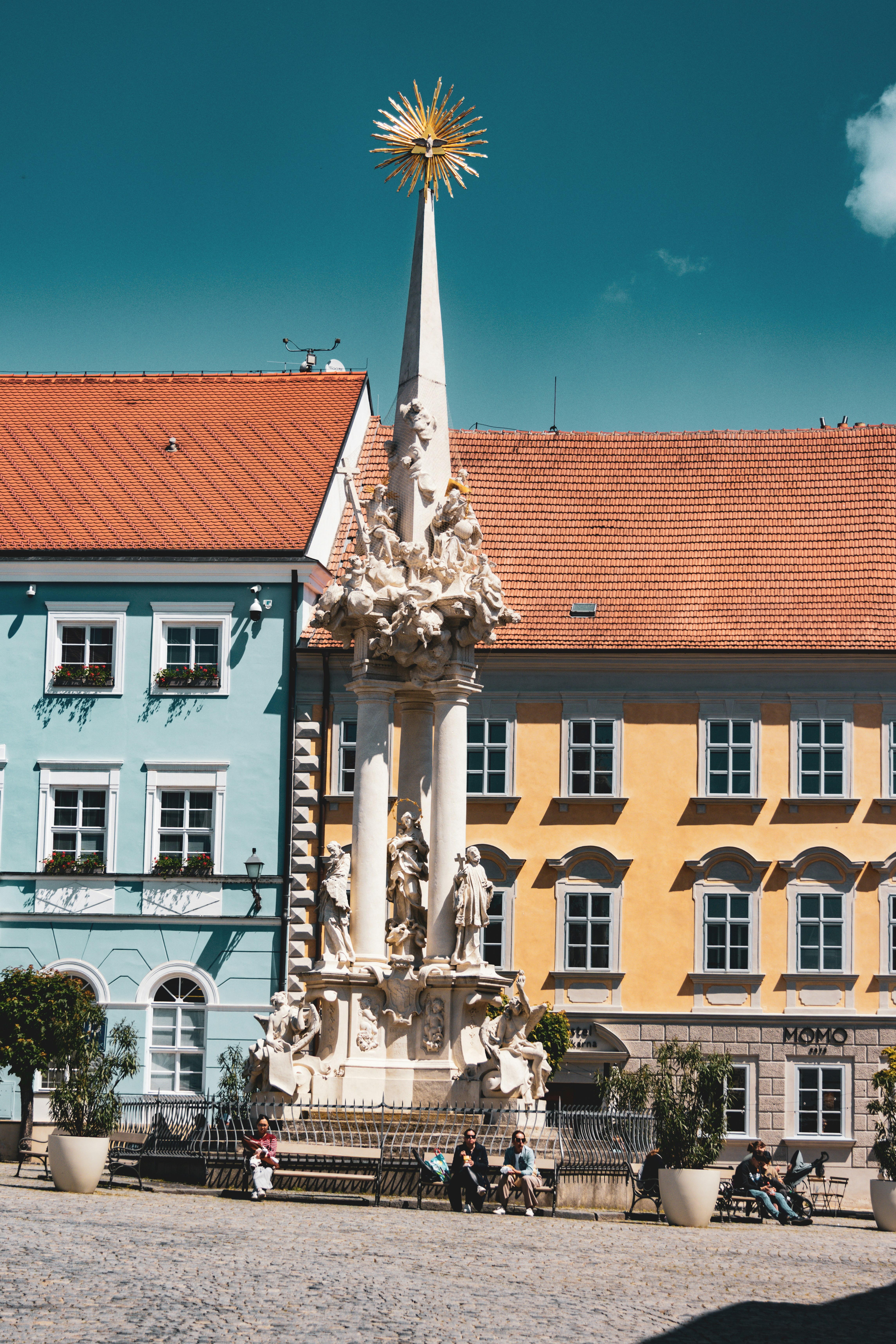 Sculpted monument rising between pastel facades under a clear blue sky