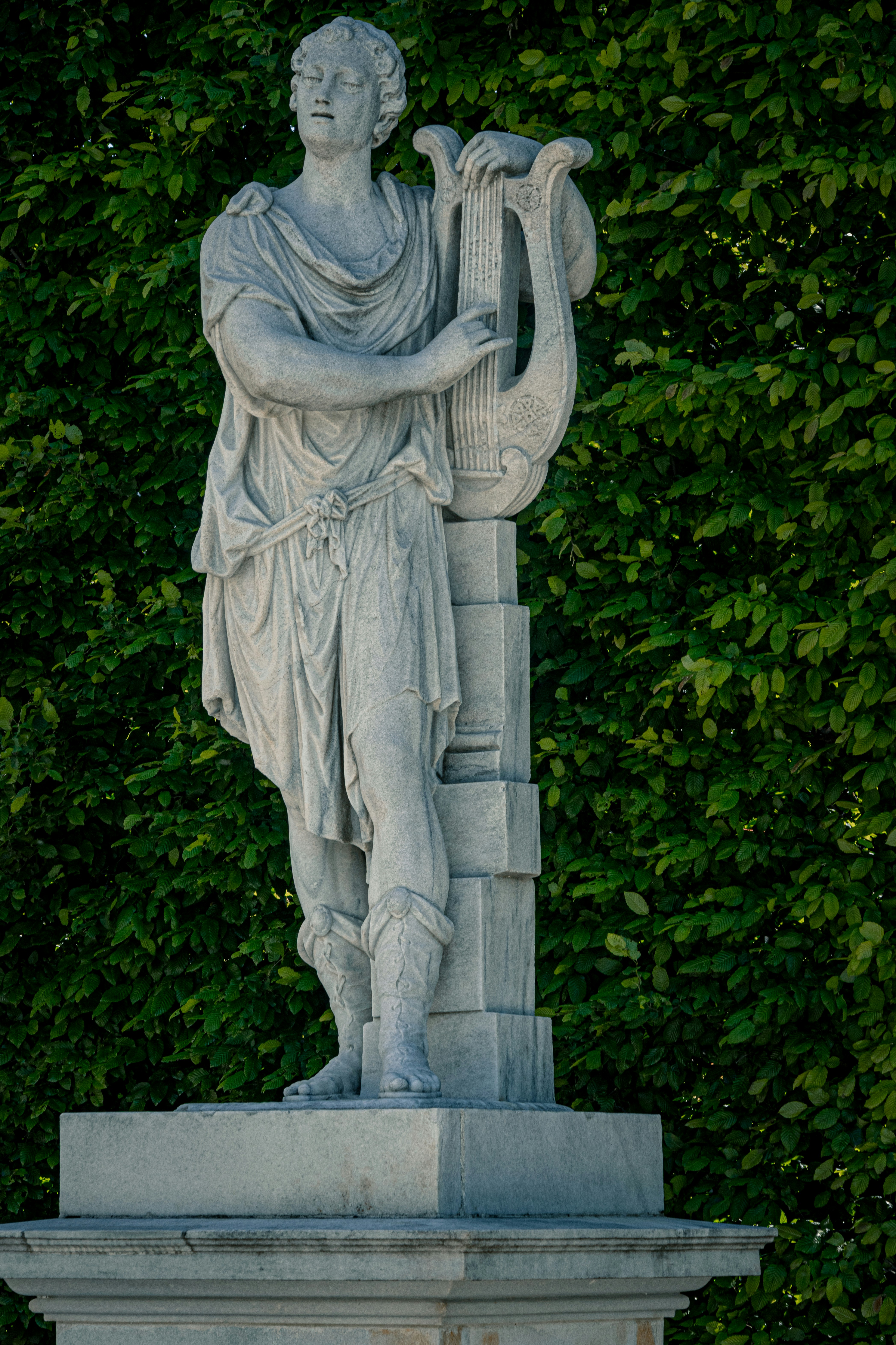 Lyre-Bearing Guardian: Classical Statue Amid Verdant Backdrop