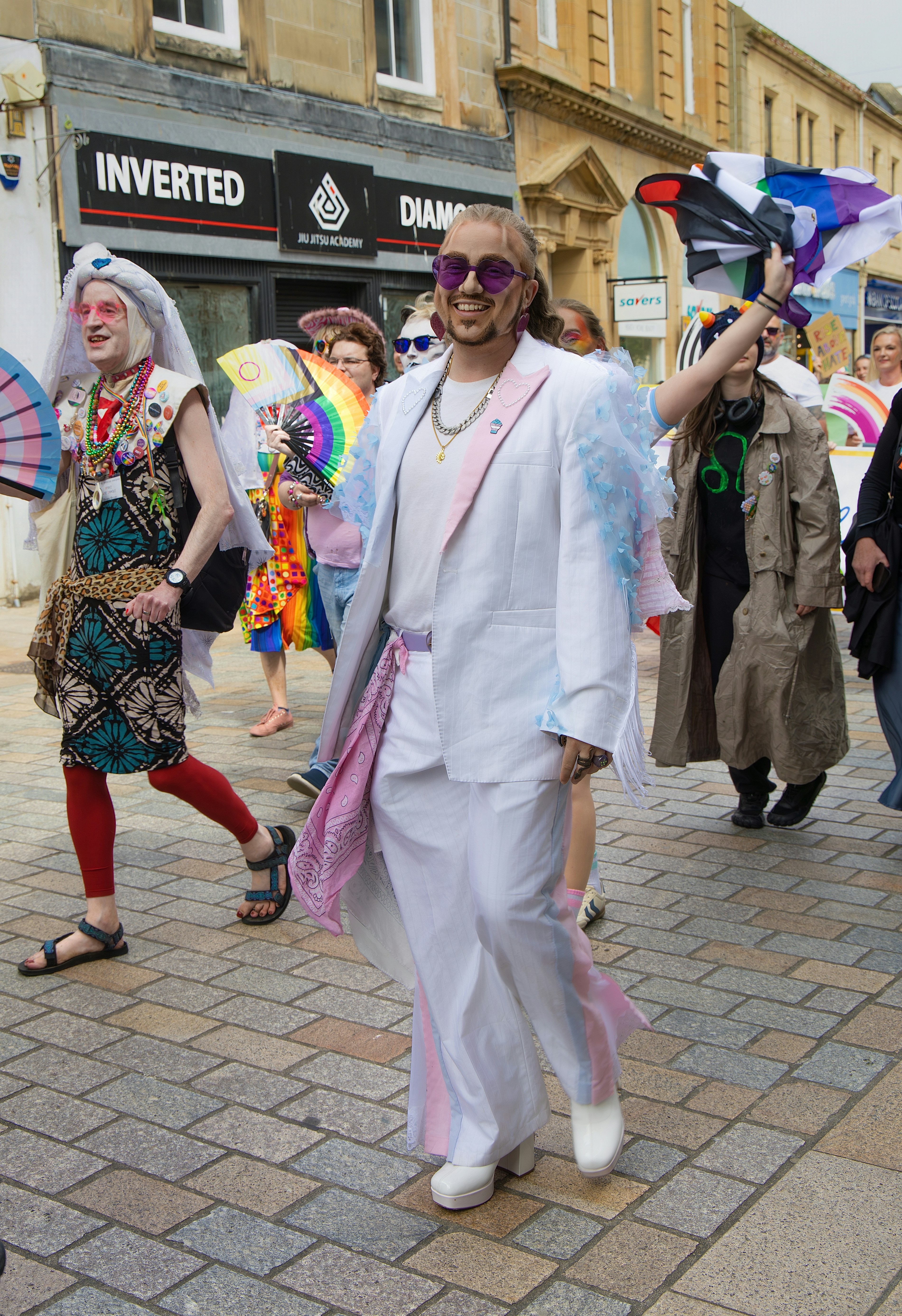 White-suited dancer leads a colorful parade through a stone-paved street
