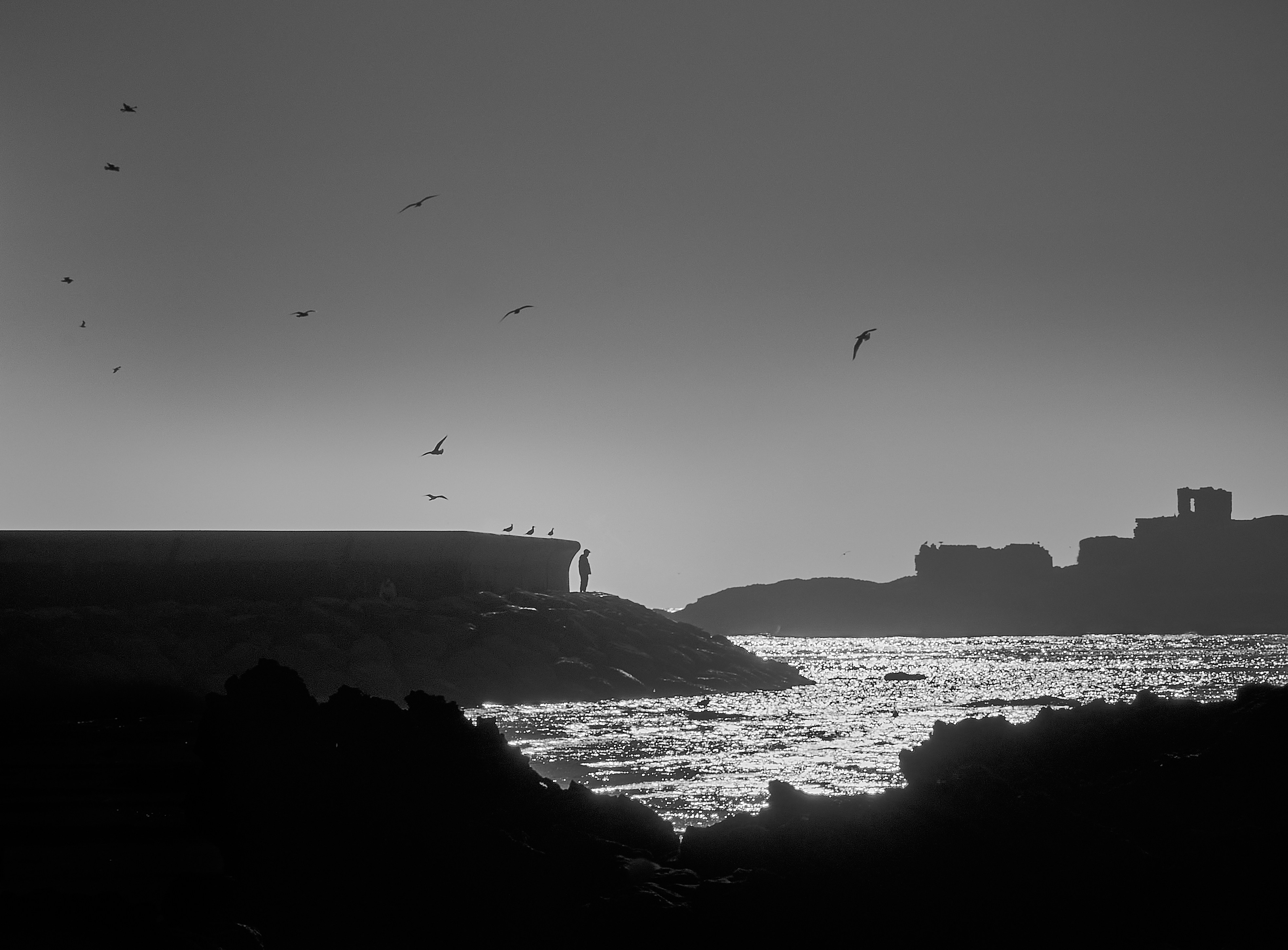 Silhouetted Promontory: A Lone Figure Against the Glimmering Sea