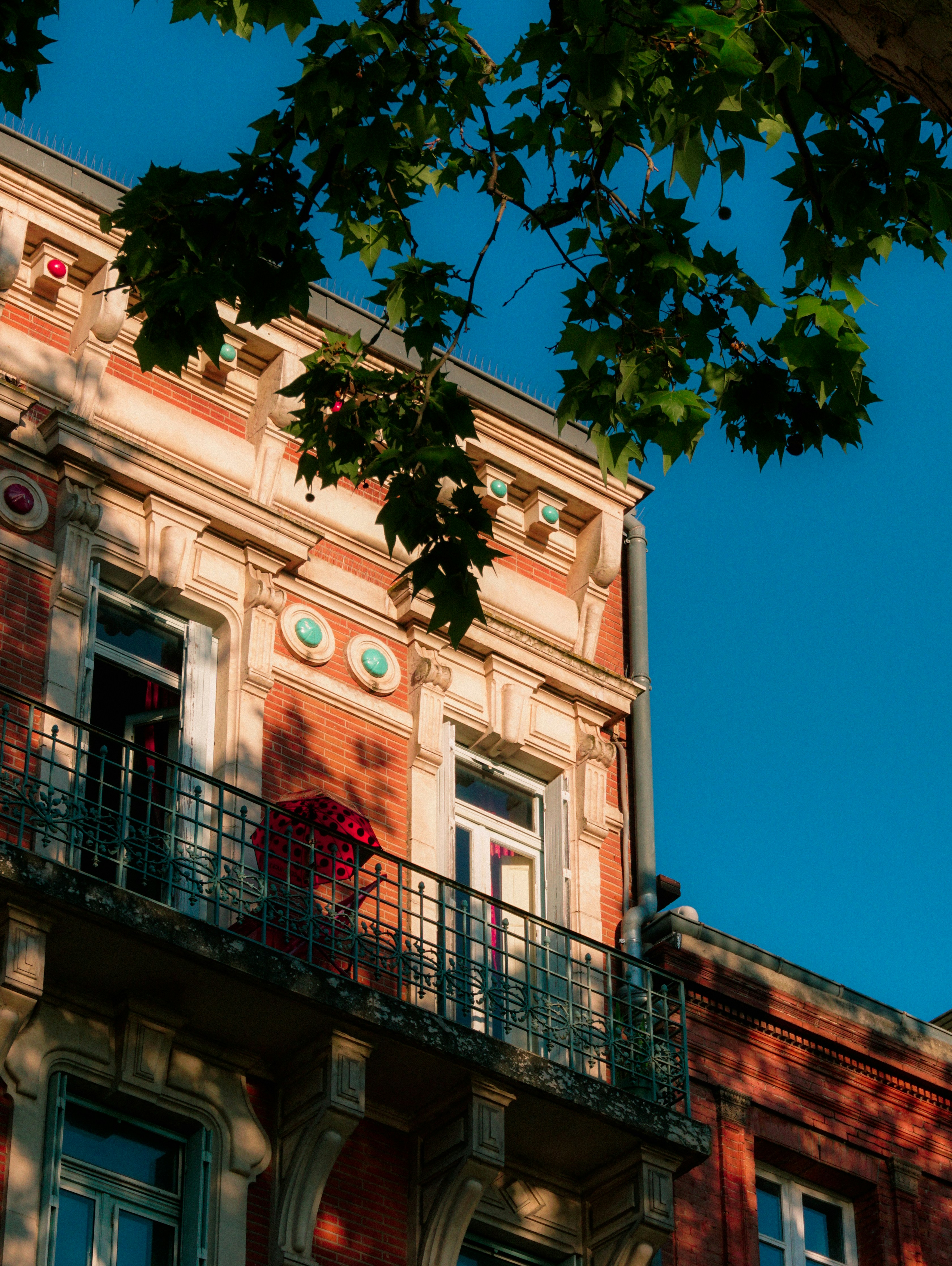 Brick Facade and Balcony Beneath a Canopy of Leaves