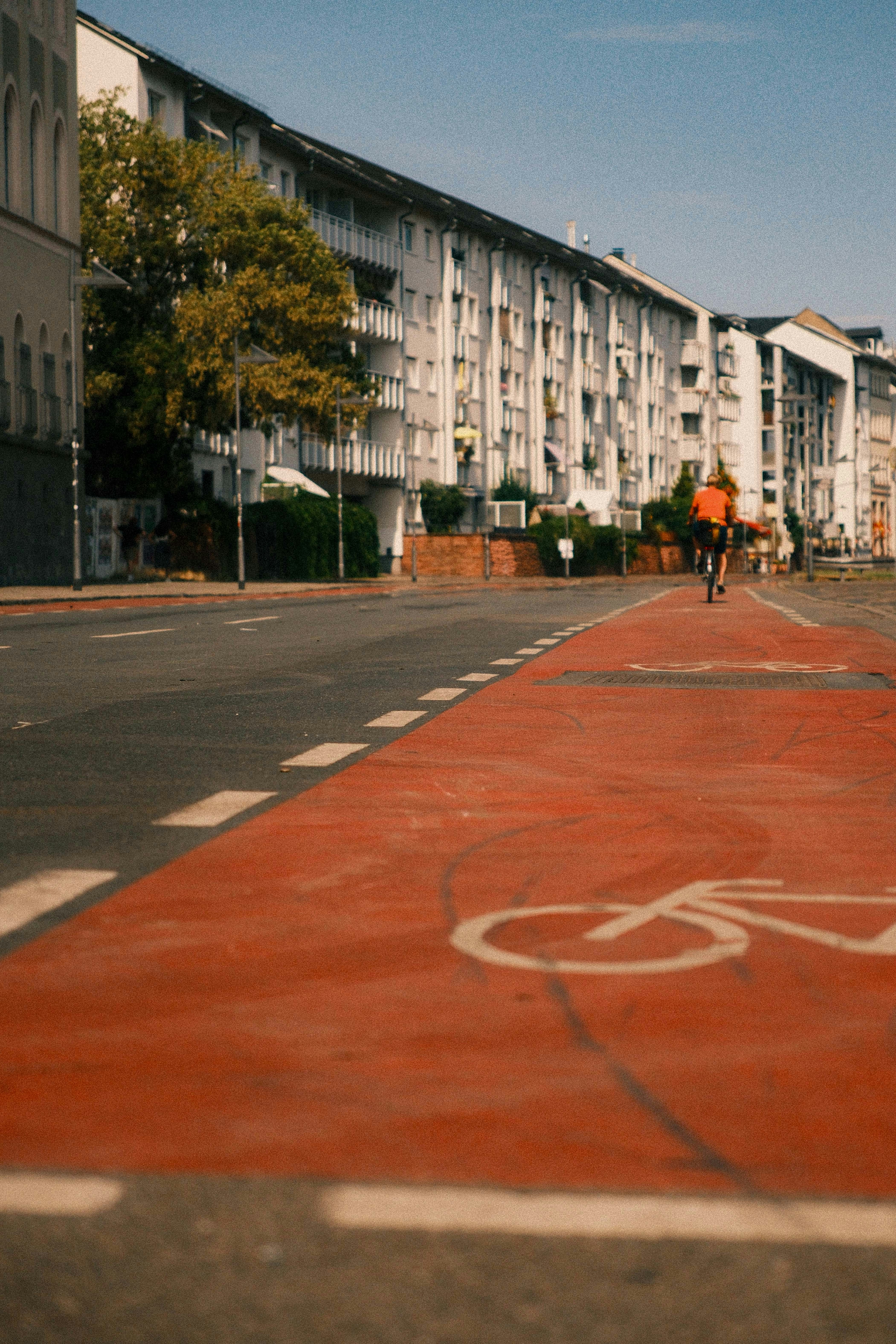 Cyclist on a red bike lane serenely passing a row of white apartment blocks