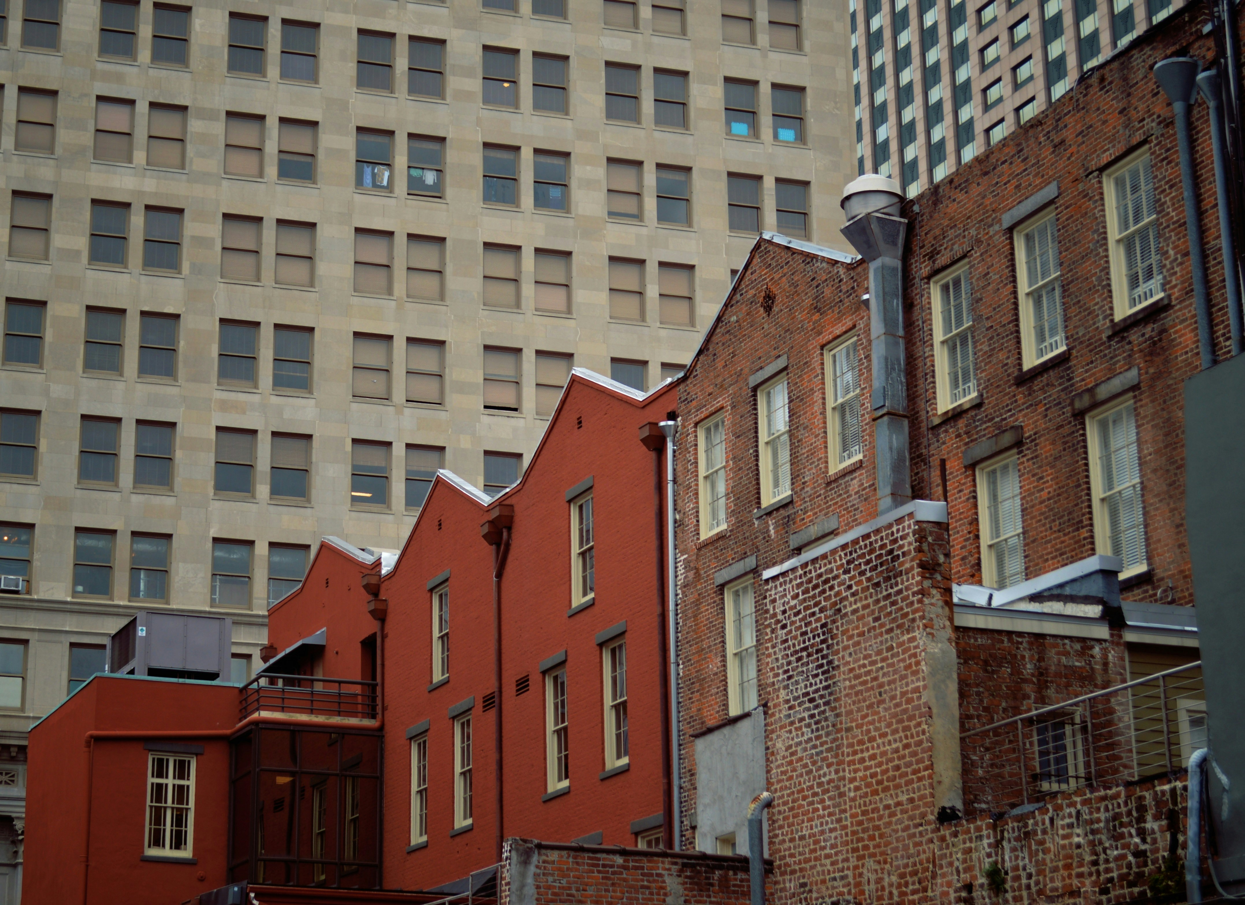 Brick rooftops and fire-escape rhythm under a gray city backdrop, capturing a dense row of red and brown facades. Aerial vantage hints at layered architectural textures.