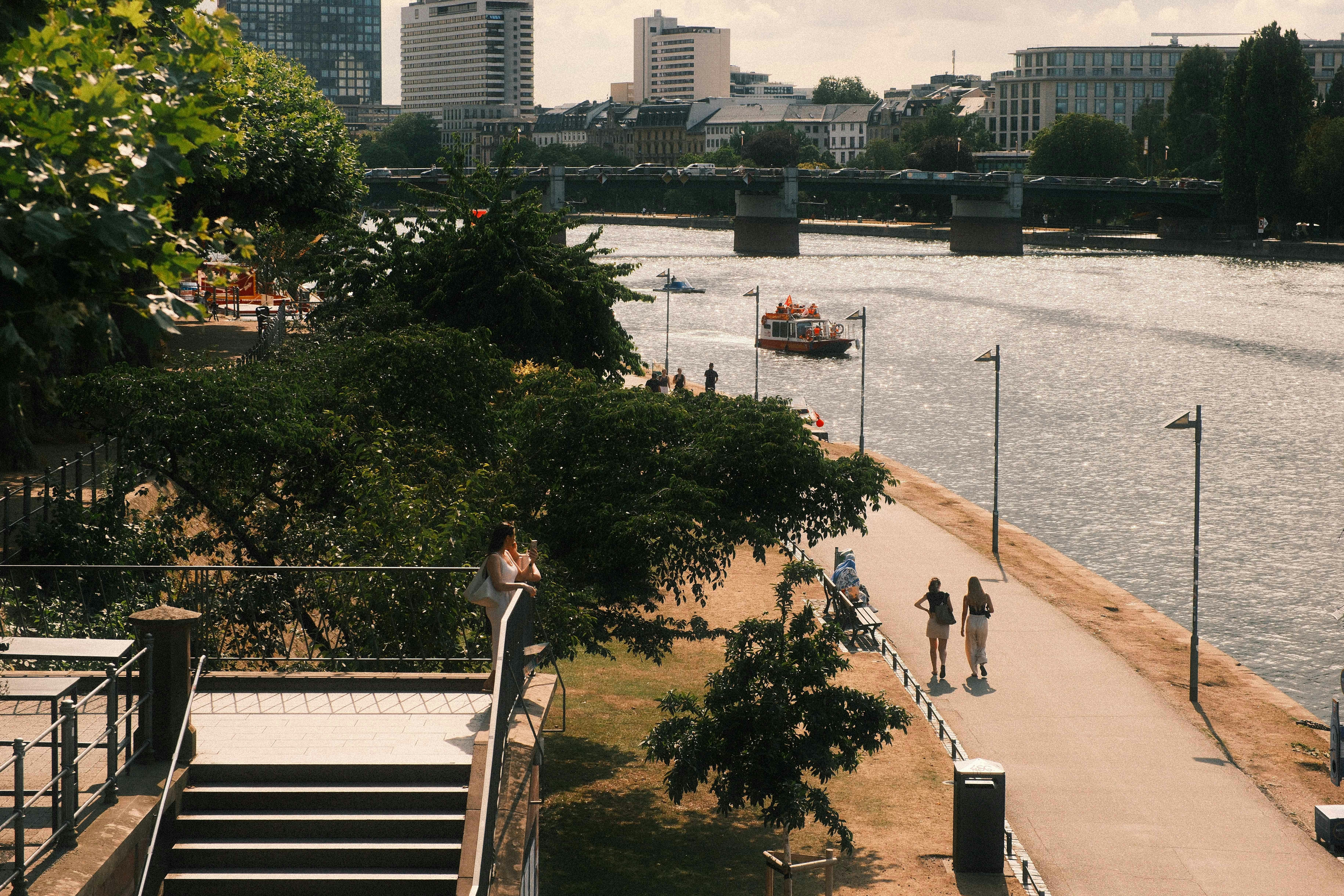 Riverfront Moment: A Sunlit Promenade Framed by Shade and Cityscapes