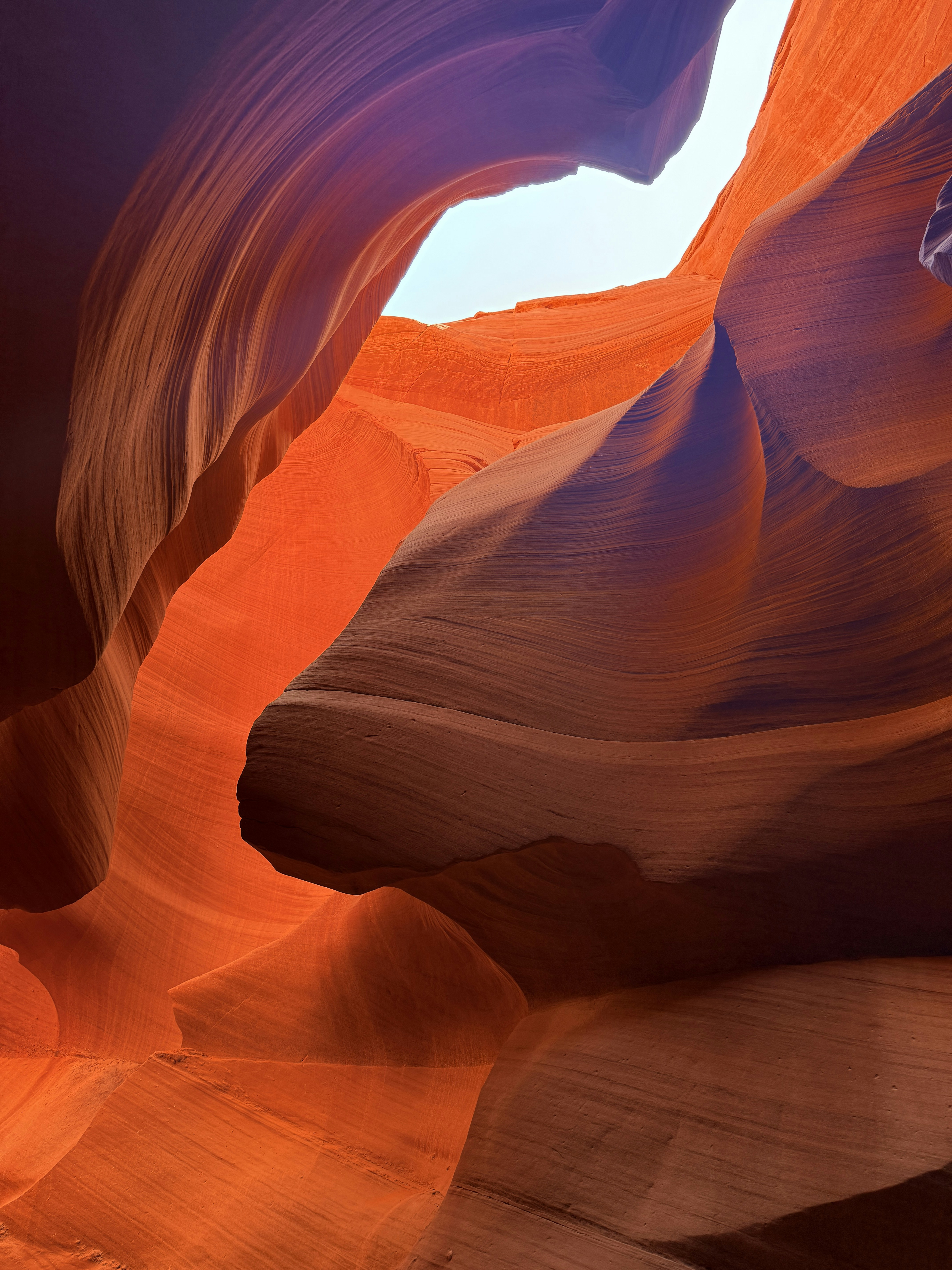 Sculpted red sandstone walls curve into a sunlit slot canyon, with warm orange light streaming through and reflecting on the smooth textures. A natural architectural wonder captured in vivid color and form.