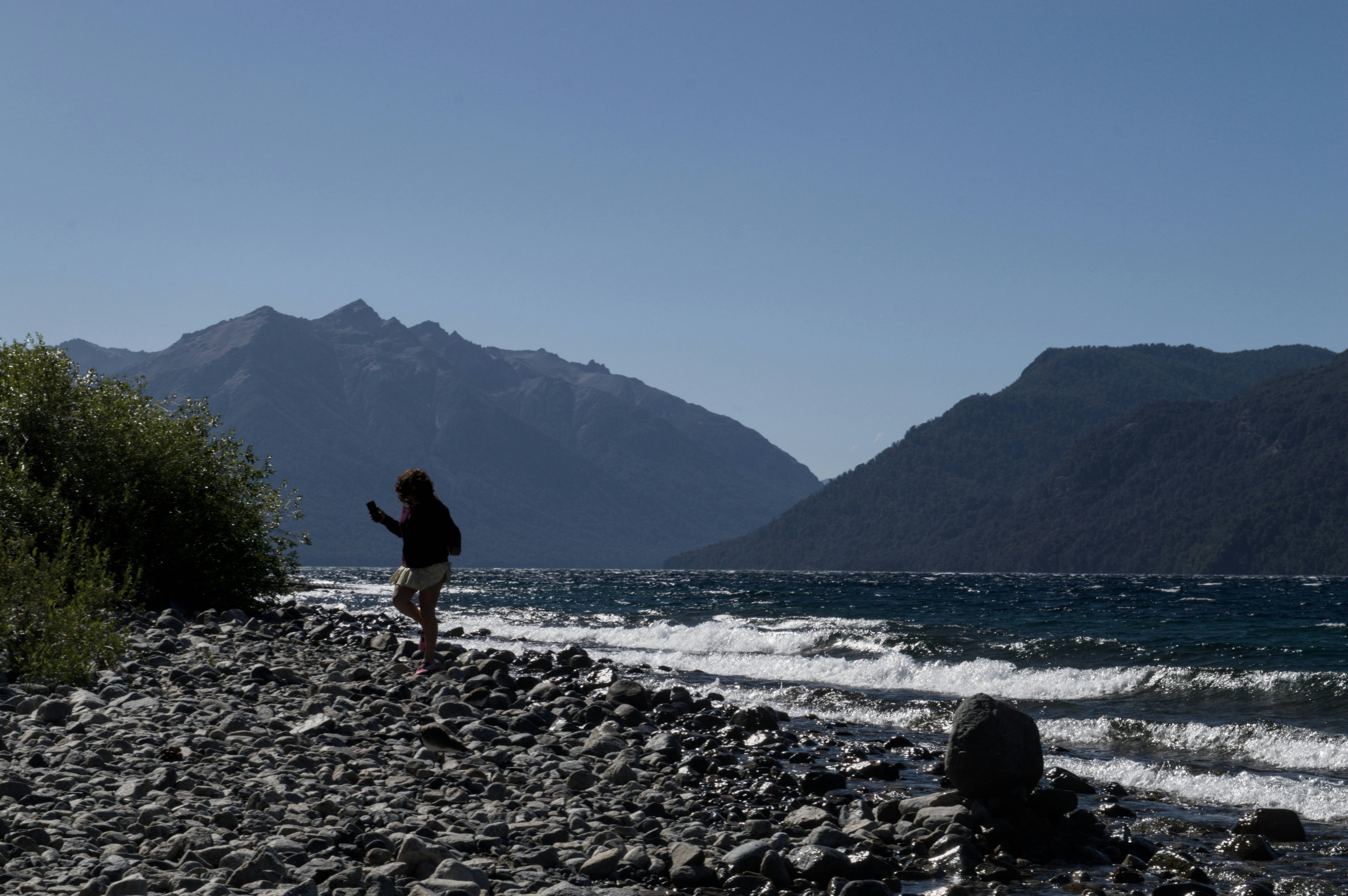 Silhouette at the Shoreline: A Lone Figure Amid Mountain Waves