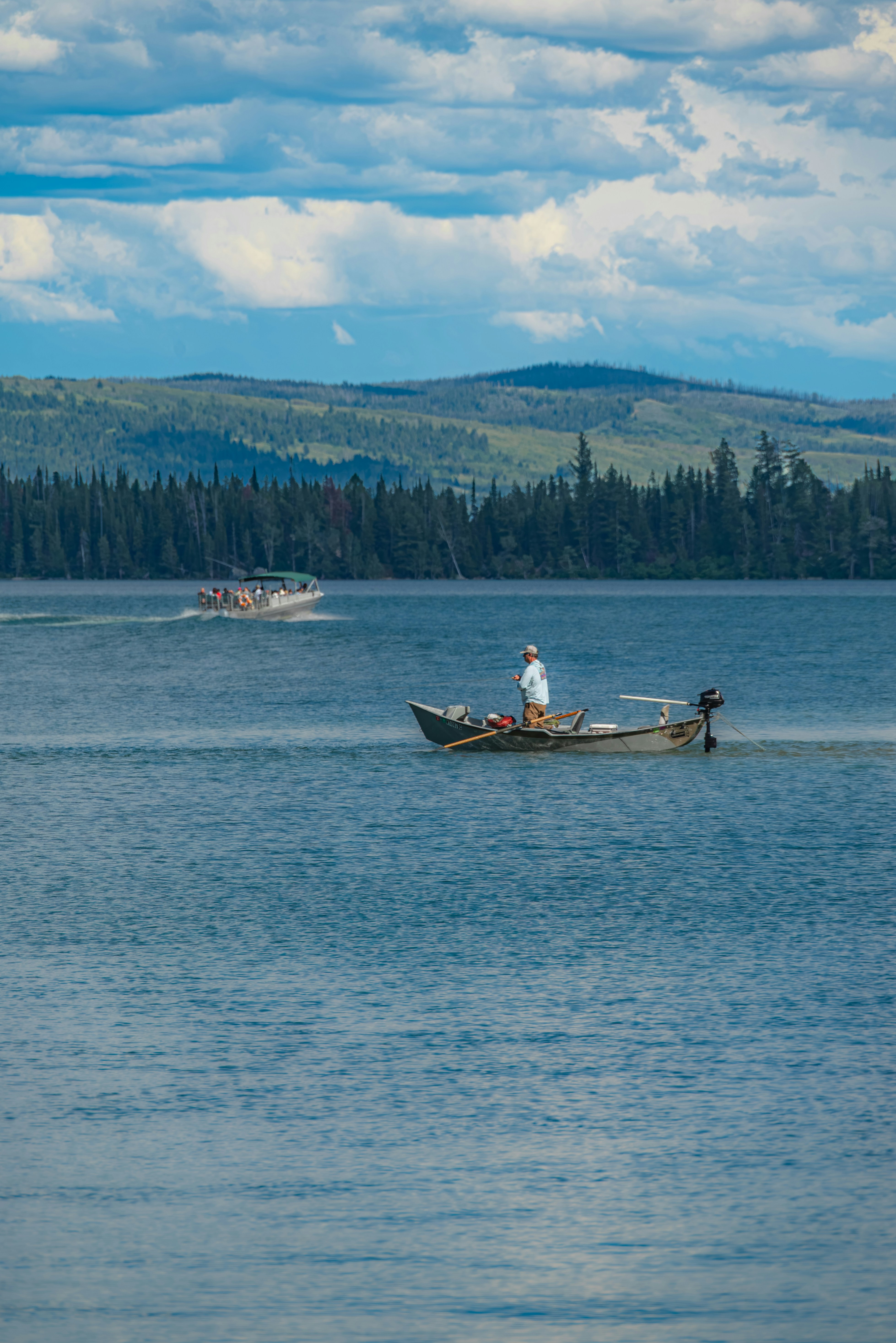 A solitary angler anchors a quiet lake as distant boats skim the horizon