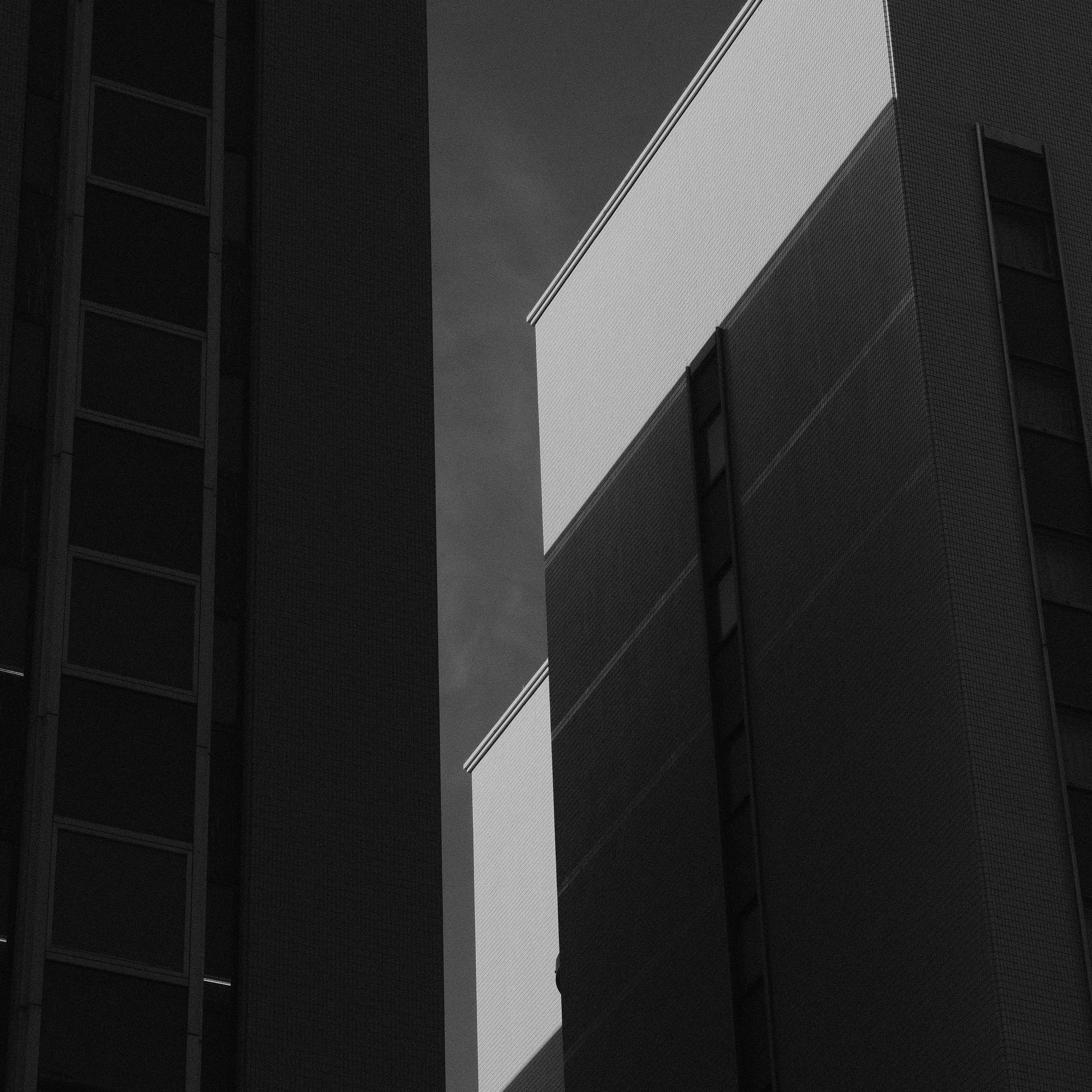 Monochrome close-up of two modern building façades with a narrow vertical gap and bright edge highlights, emphasizing geometric planes and negative space. Abstract architectural detail devoid of people.